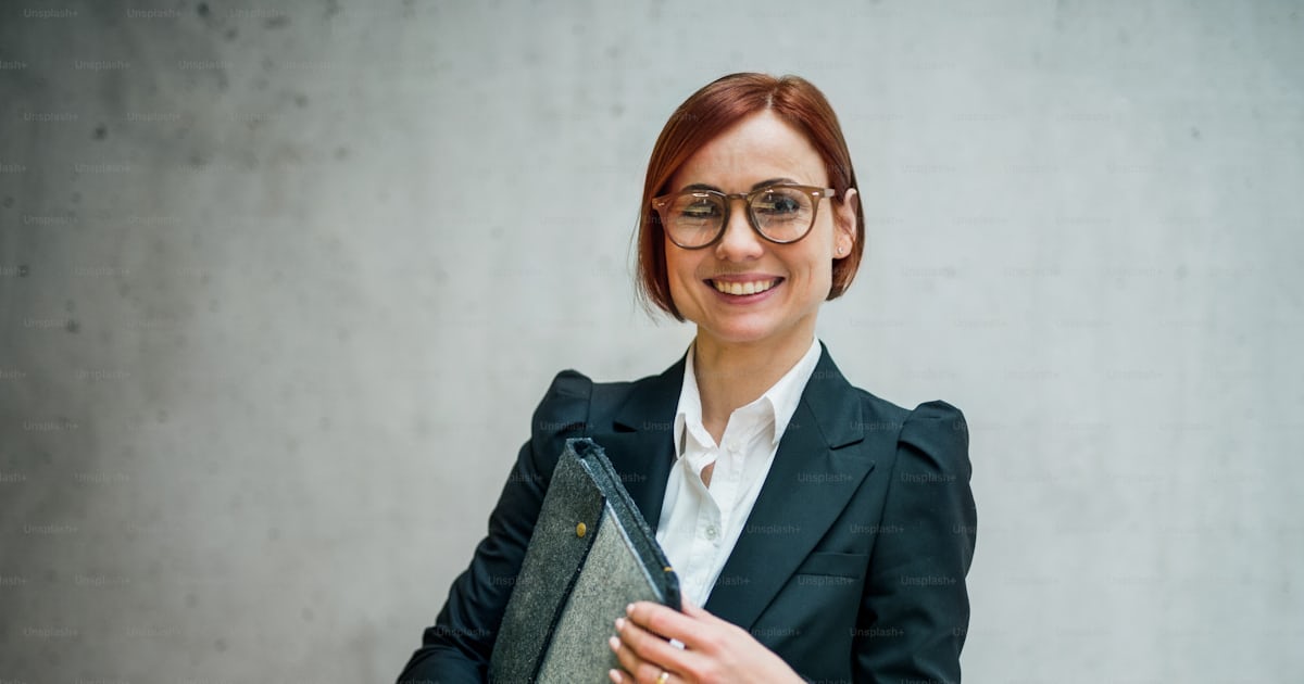 A Portrait Of Young Cheerful Businesswoman Standing In Office Looking