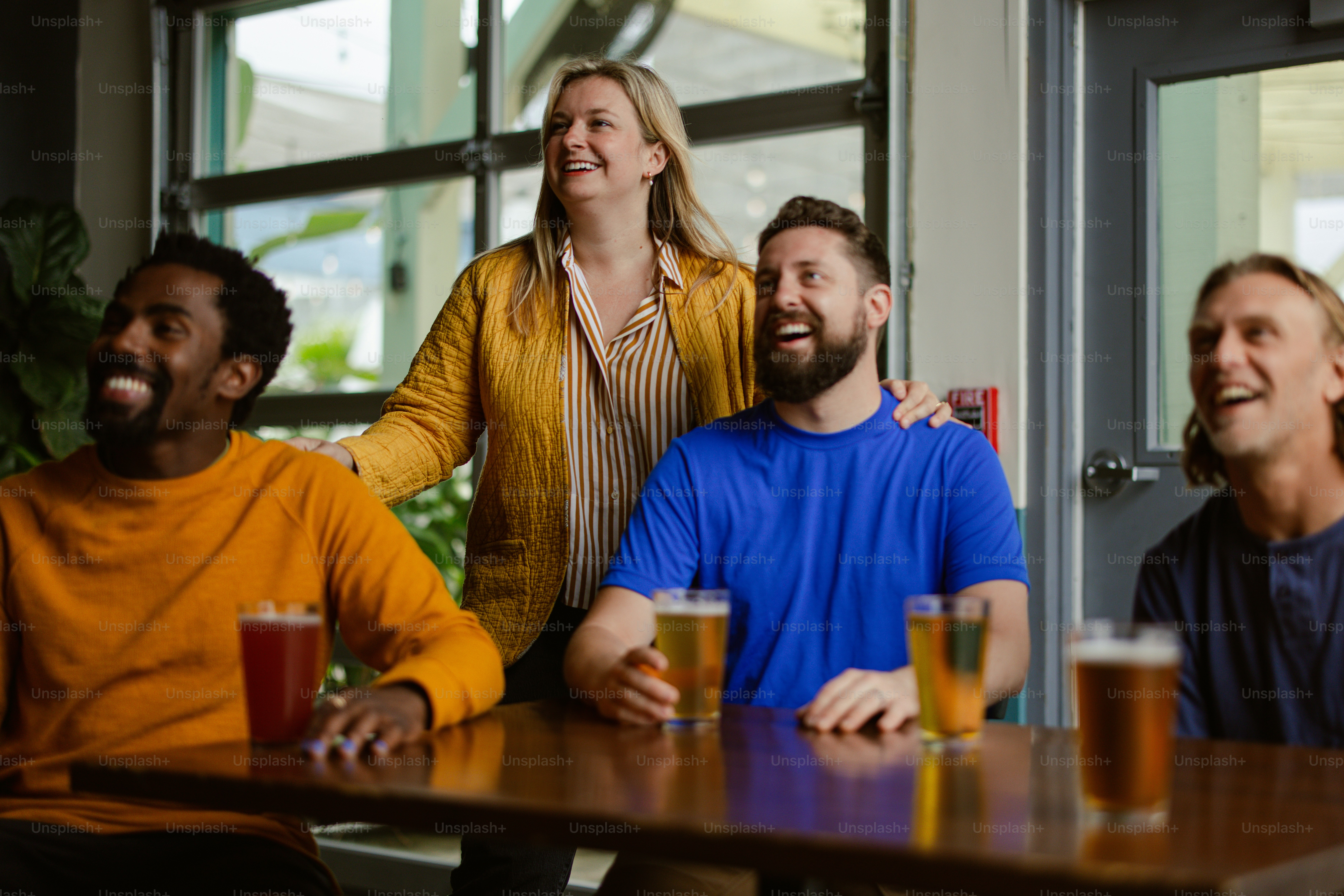 A group of people sitting around a table with beers photo – Sports bar ...