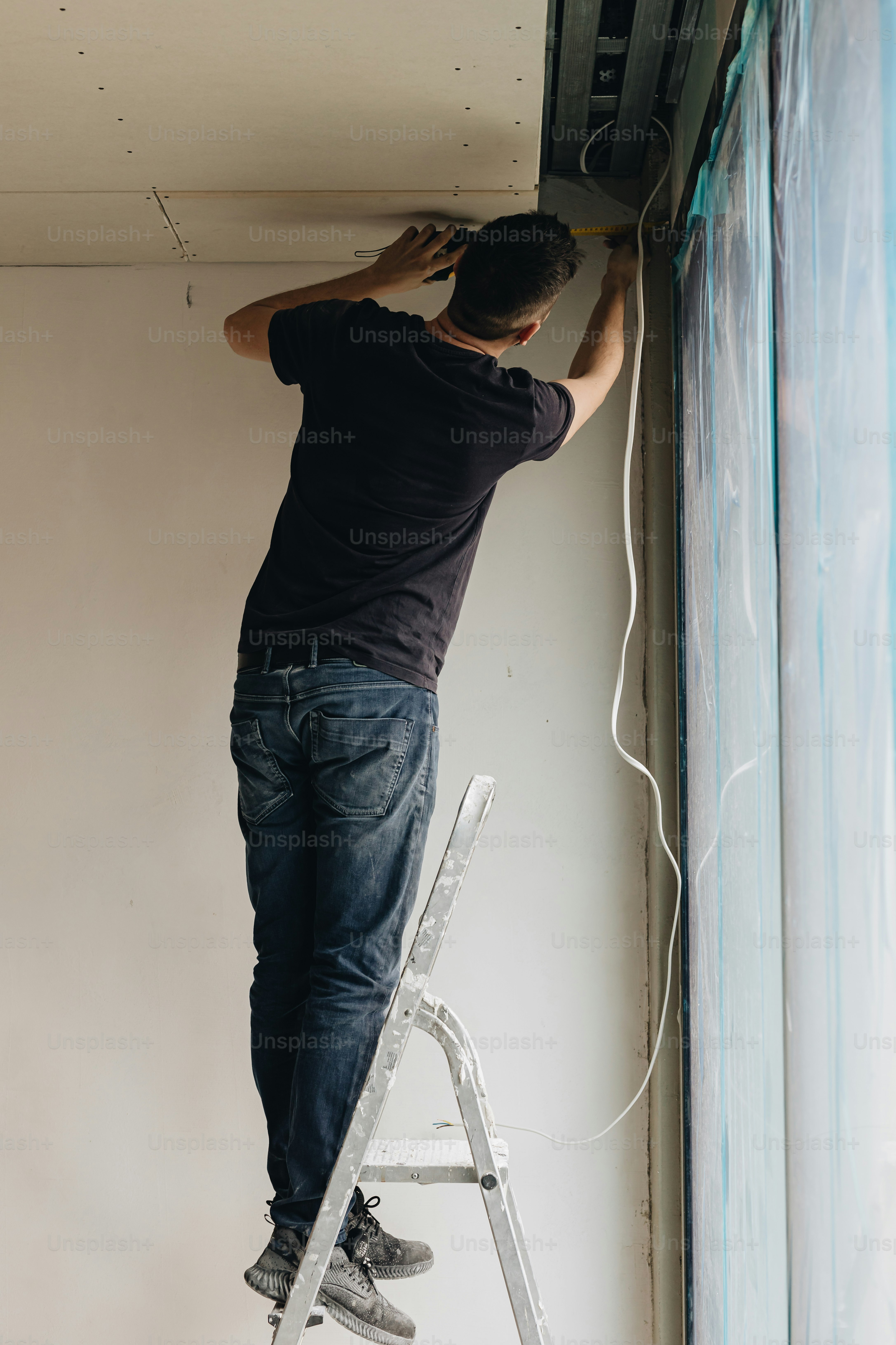 A man standing on a stepladder fixing a light fixture photo ...