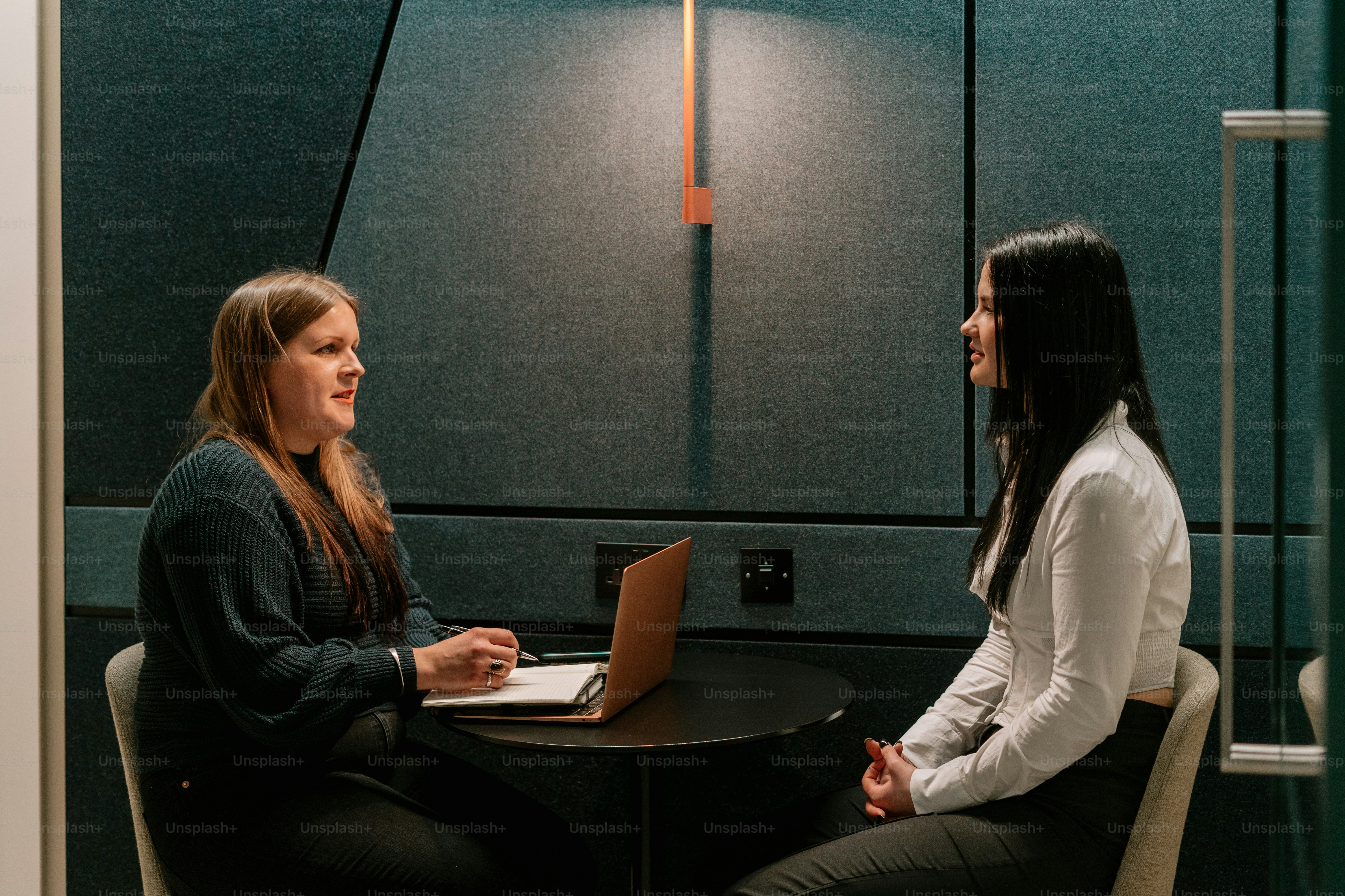 Two women sitting at a table talking to each other photo – Office Image ...