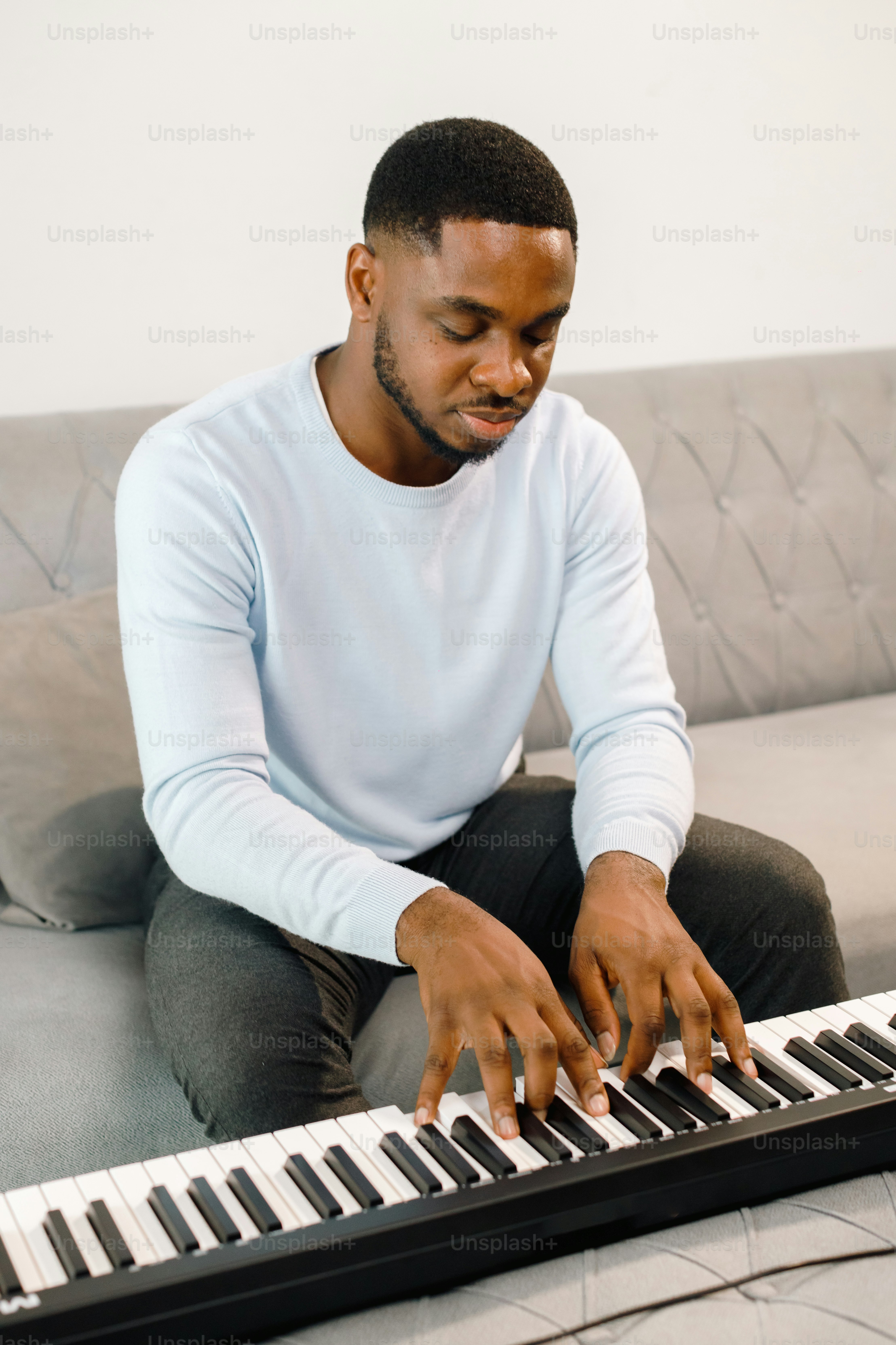 A man sitting on a couch playing a keyboard photo – Making music Image ...