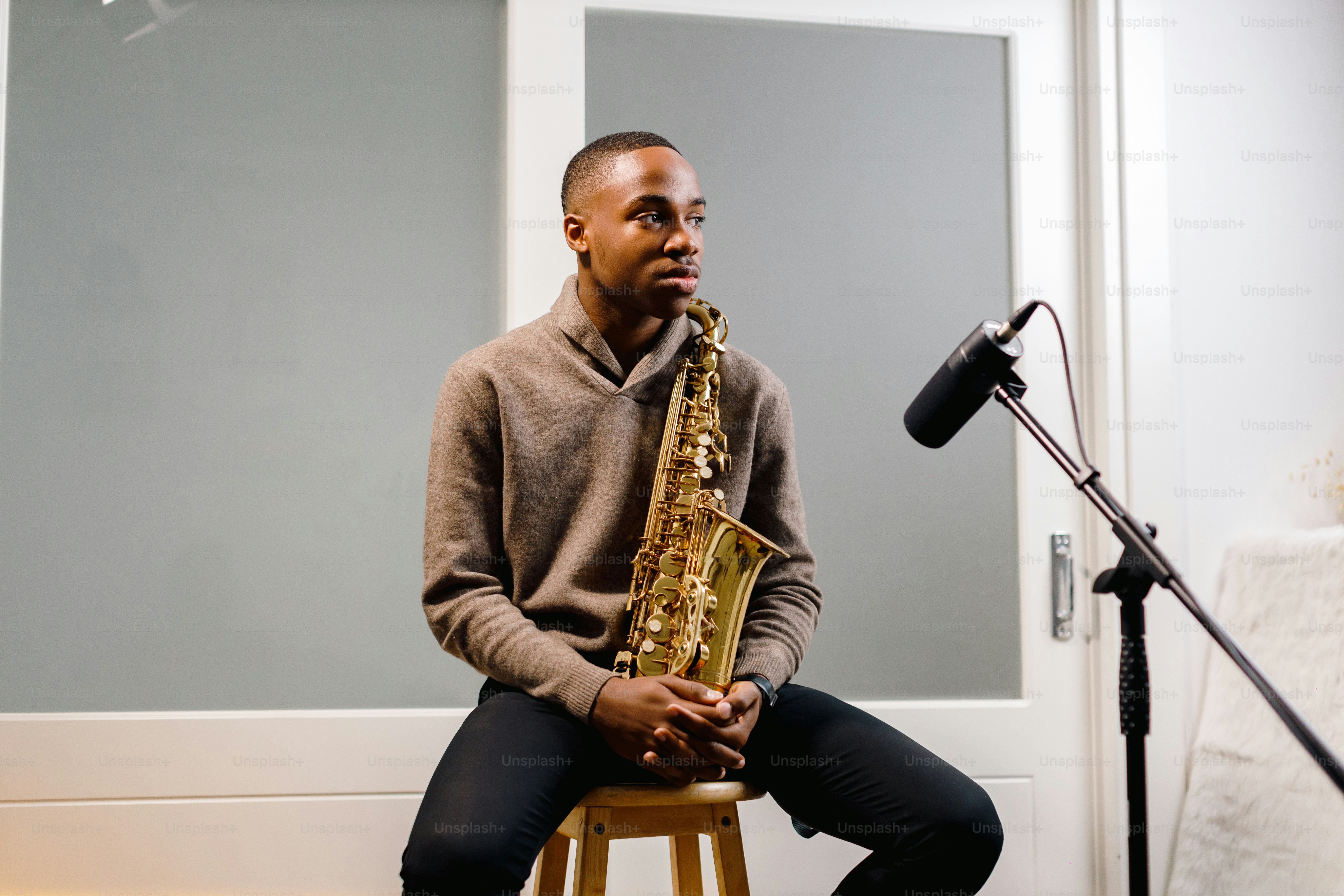 A man sitting on a stool holding a saxophone photo – Music Image on ...