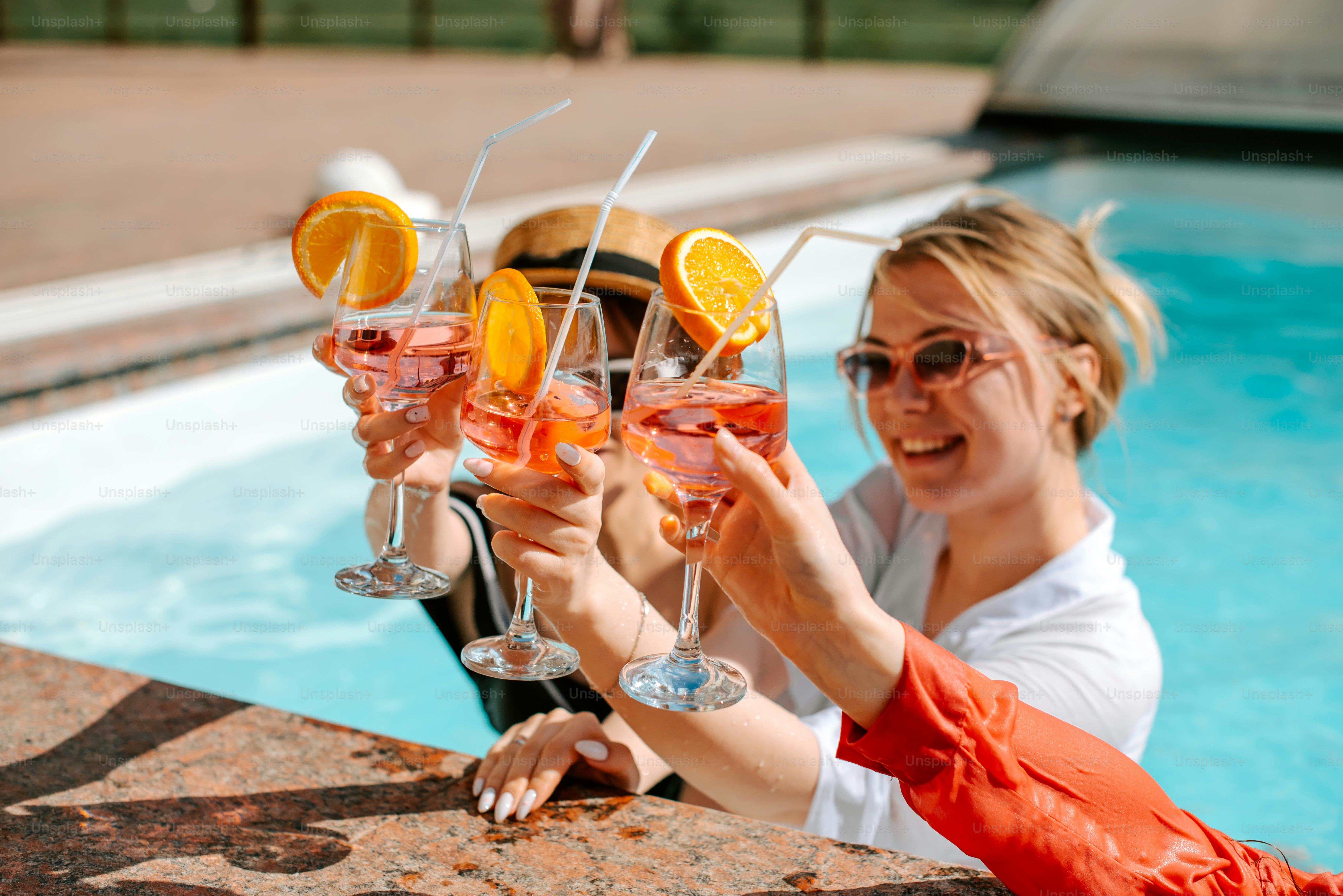 A group of people toasting with drinks in a pool photo – Summer parties ...