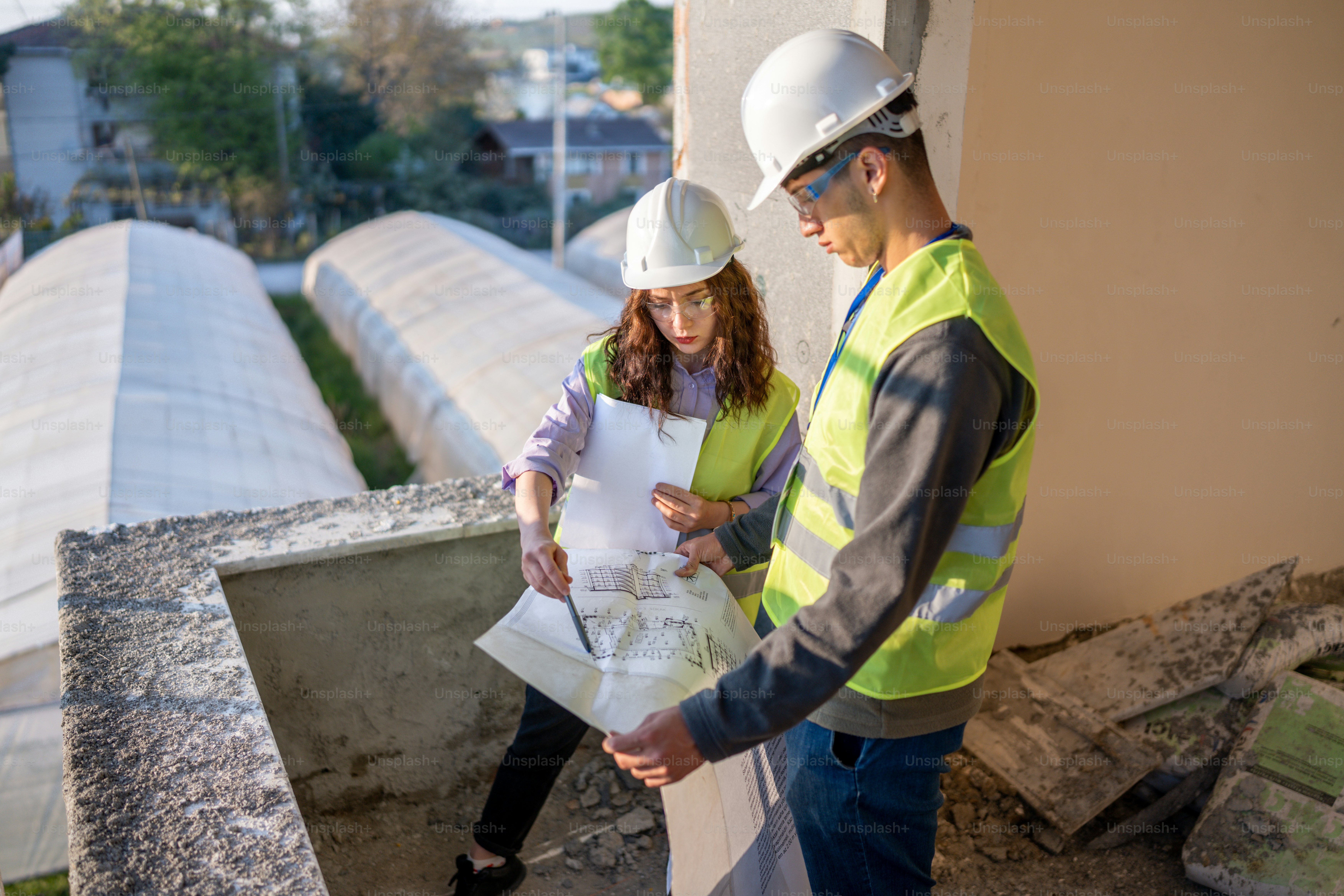 A man and a woman in safety vests are looking at a blueprint photo ...
