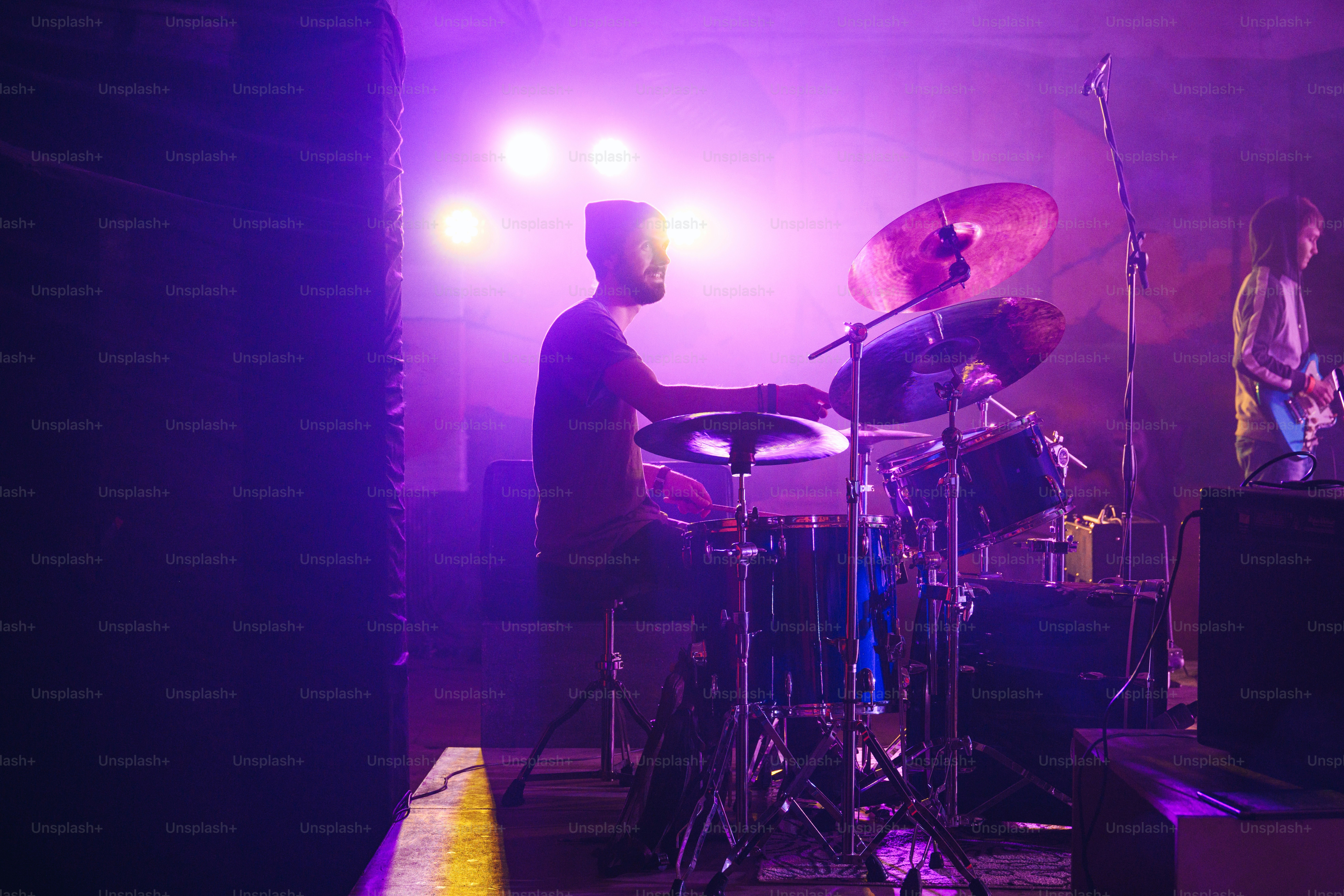 A man playing drums in front of a purple light photo – Music Image on ...