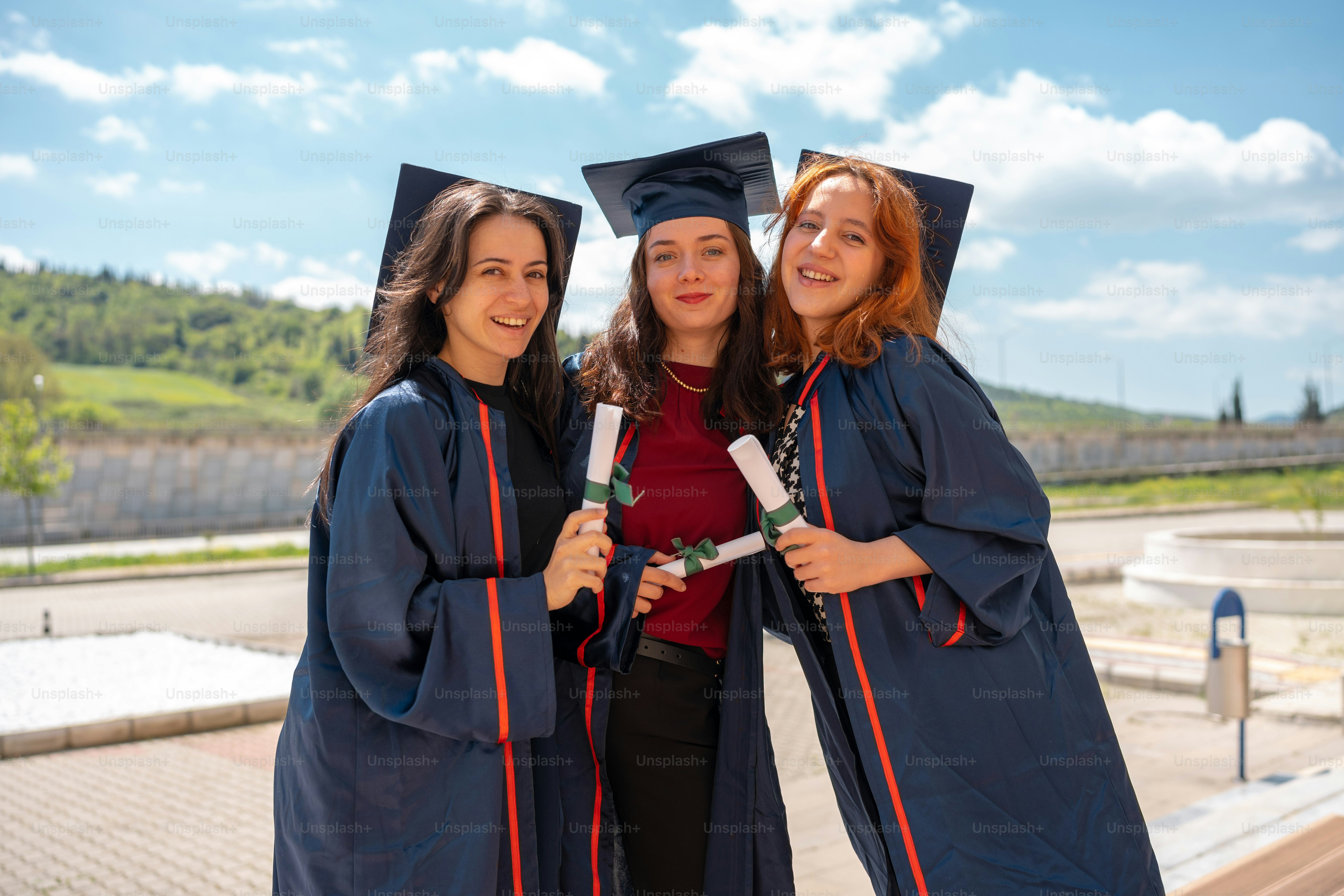 Two girls in graduation gowns holding up their hats photo – Graduate ...