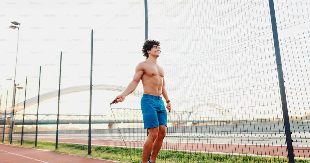 스포티한 백인 웃는 셔츠를 입지 않은 남자가 아침에 철조망 옆에서 법정에서 줄넘기를 하고 있다 사진 Unsplash의 이완