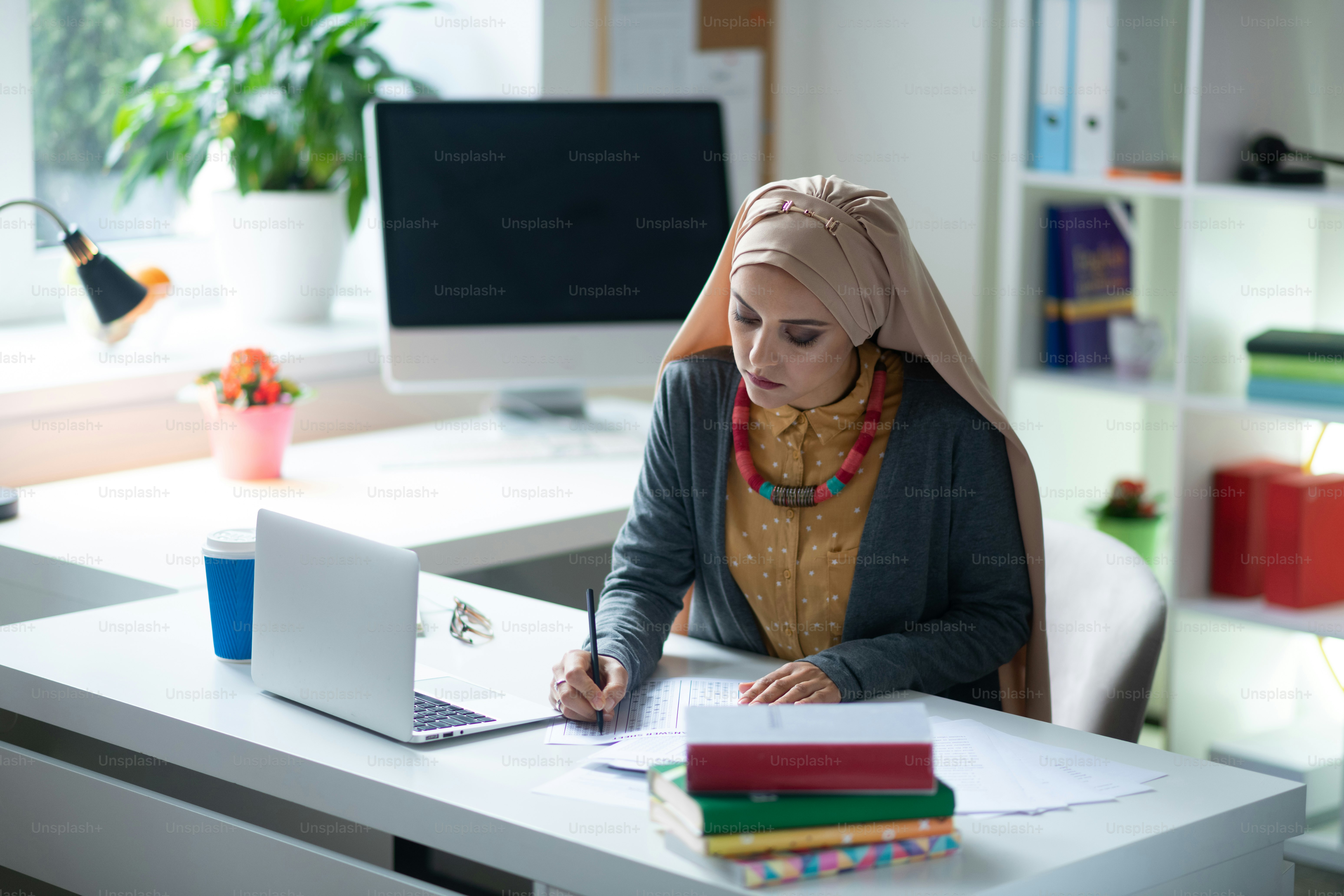 Hard-working teacher. Busy hard-working Muslim teacher sitting at the ...