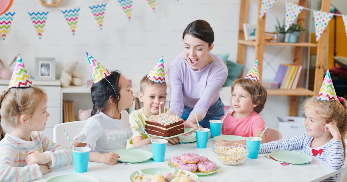 생일 케이크를 들고 촛불을 바라보는 황홀한 젊은 여성 어린 소녀 중 한 명이 친구들 사이에서 서빙 테이블로 촛불을 불고 있다