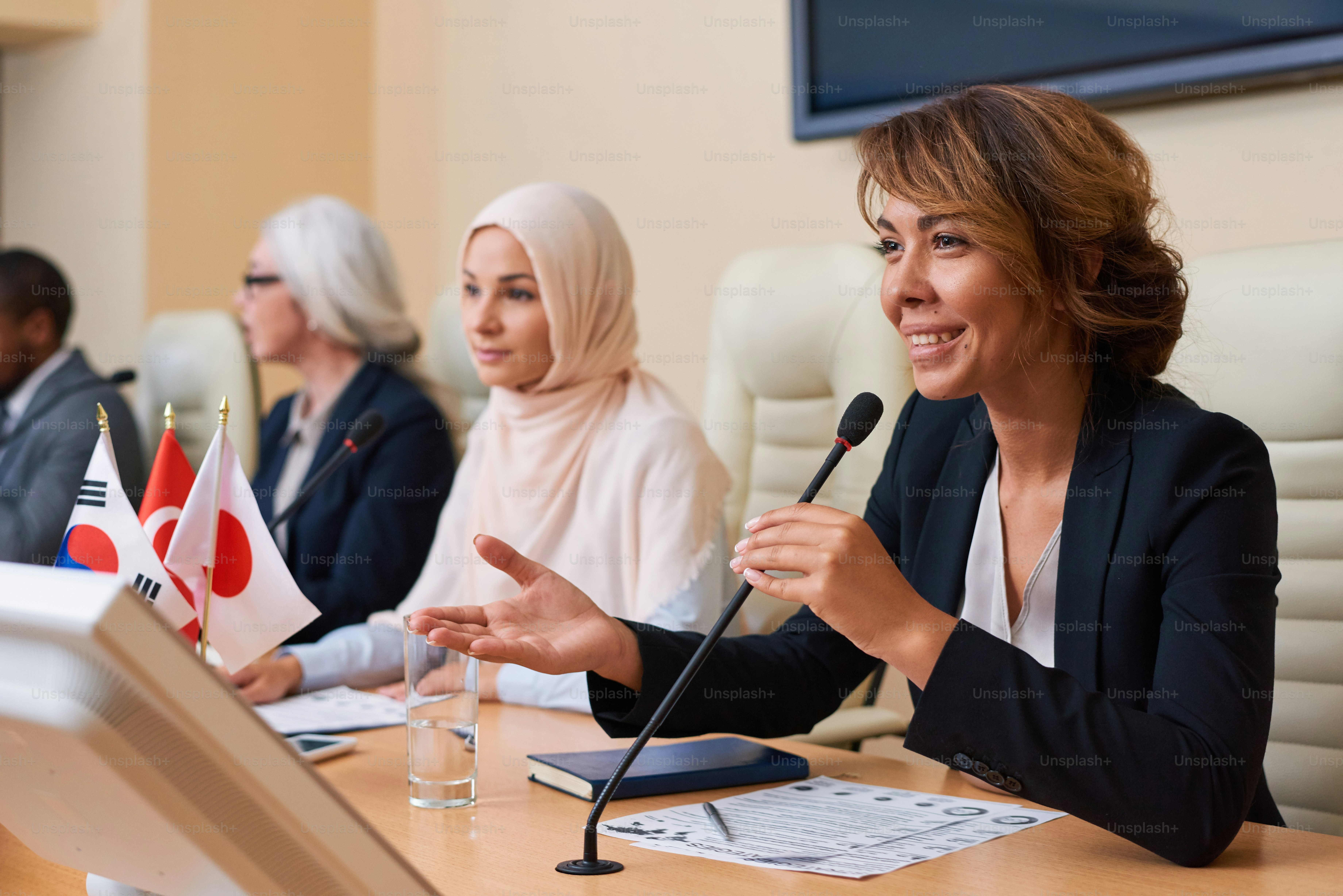 Happy young female delegate in formalwear looking at audience while ...