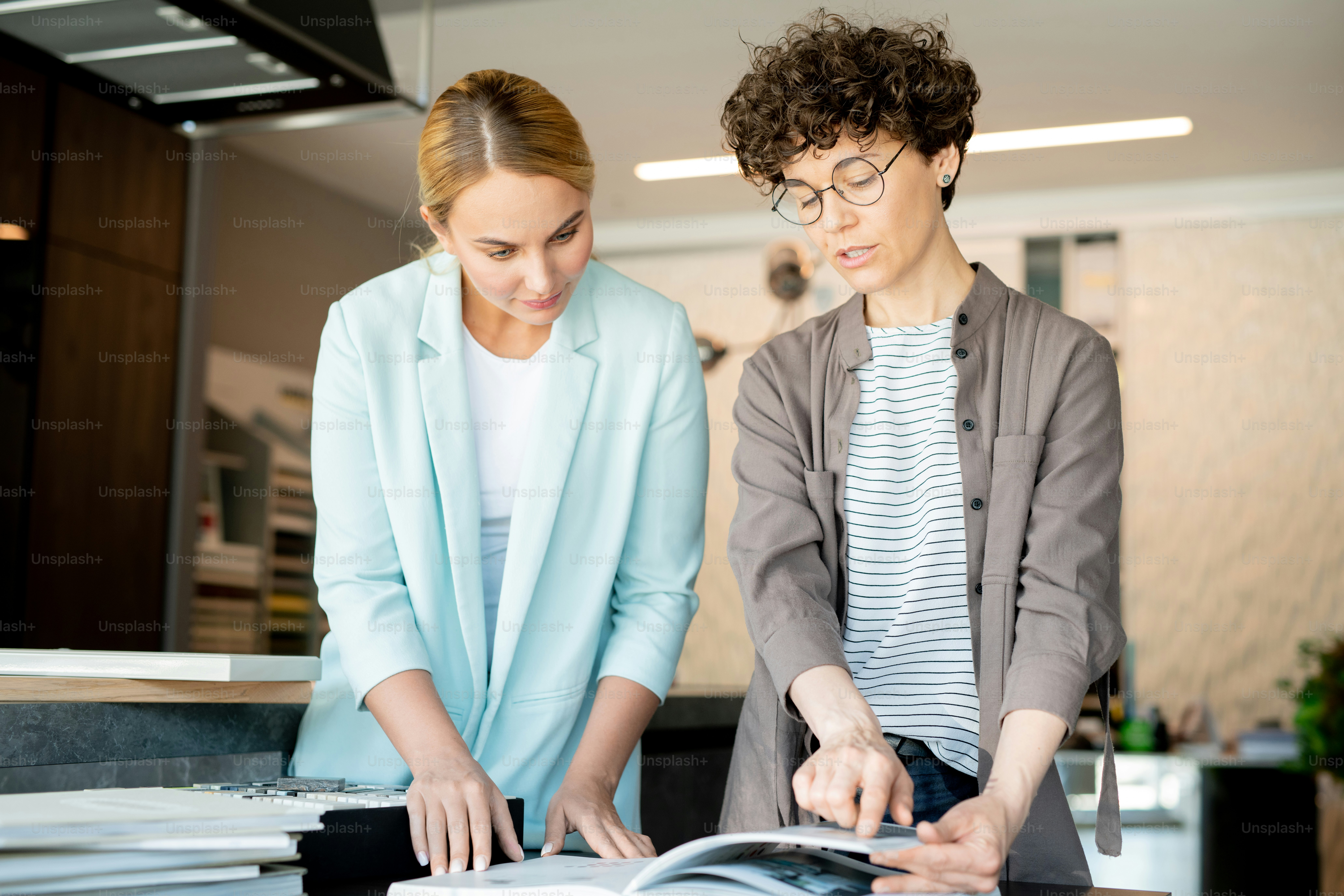 Young creative designer pointing at page of catalogue while helping ...