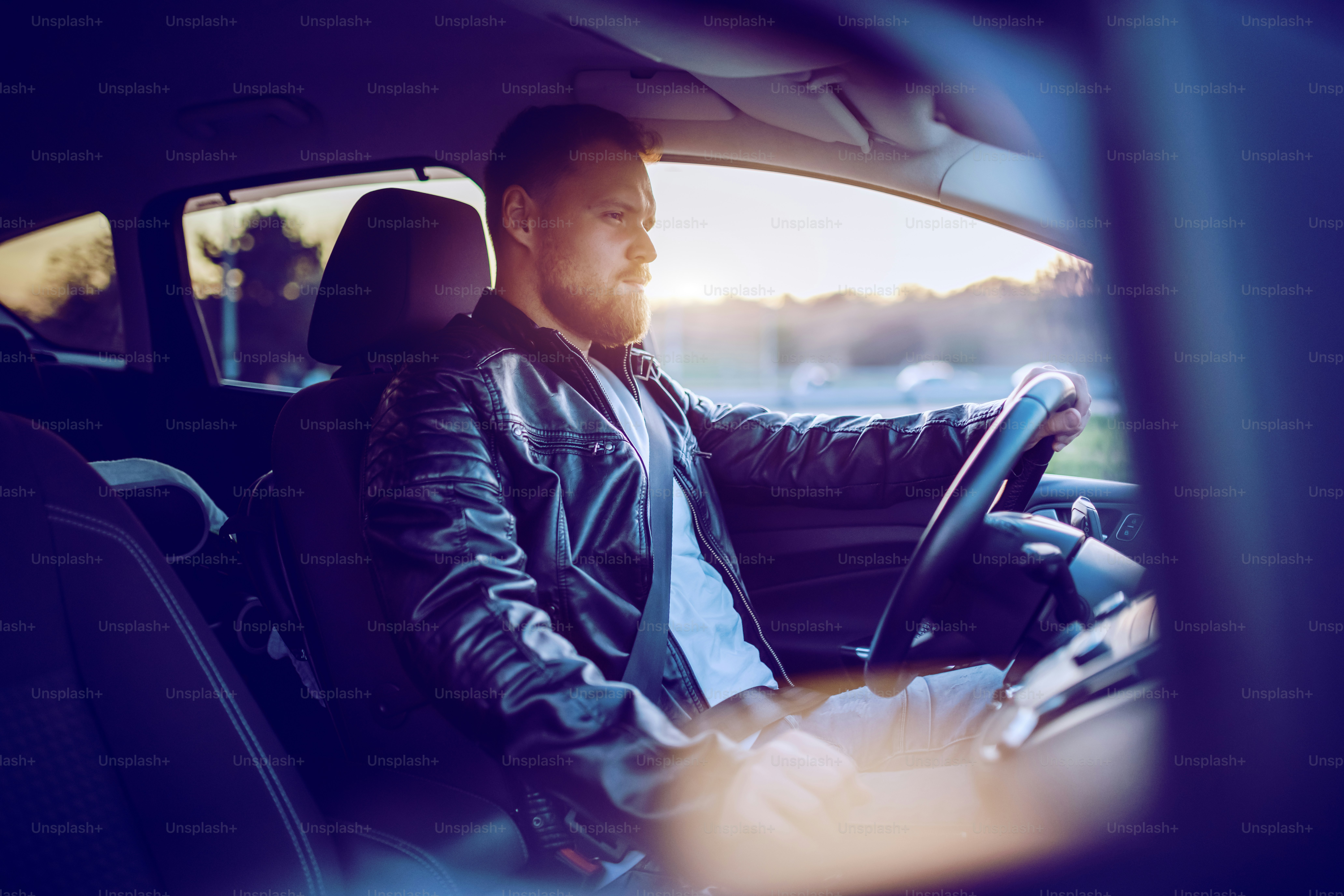 Young attractive Caucasian bearded blond man in leather jacket driving ...