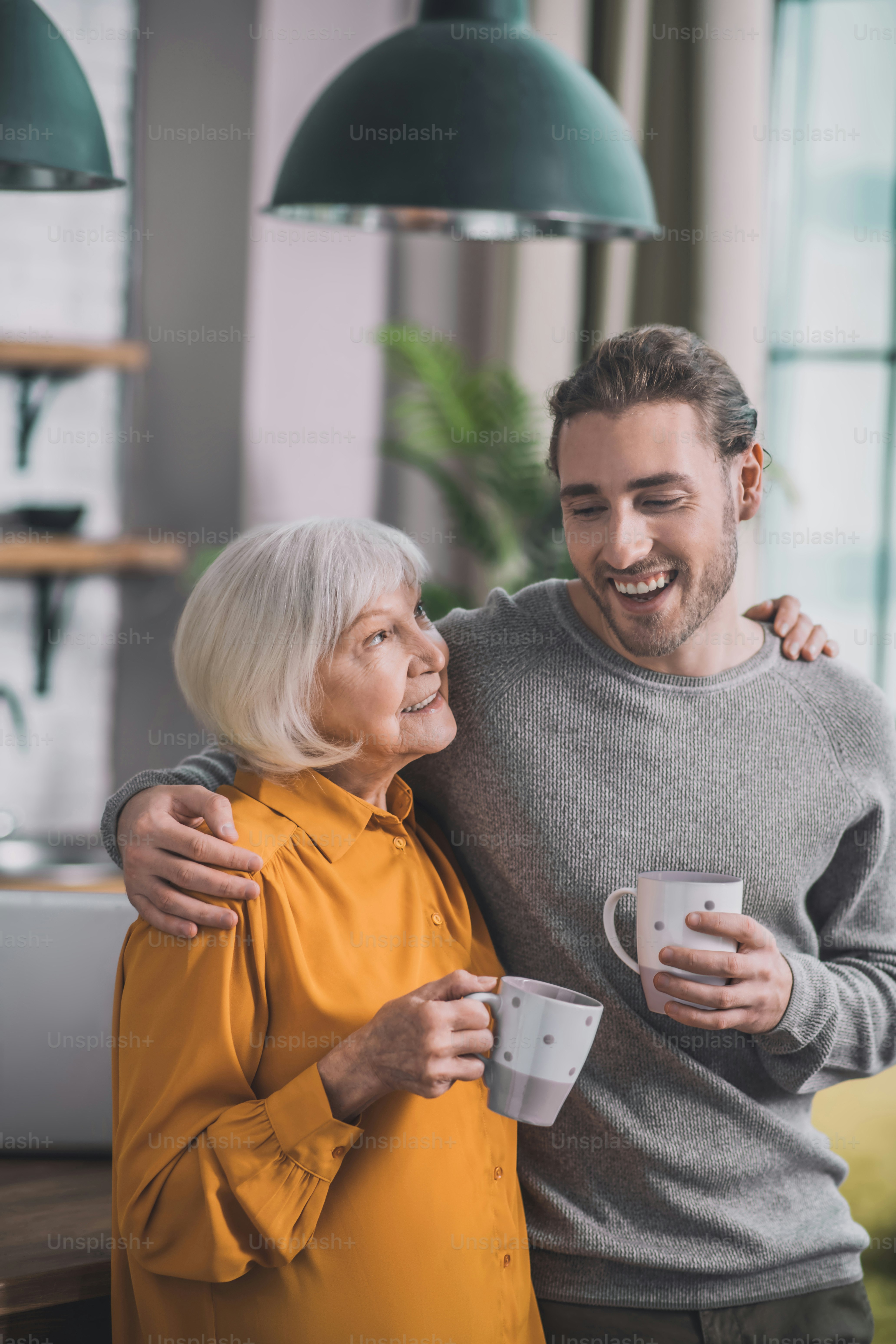 Feeling happy. Young handsome man in grey shirt and his mom feeling ...