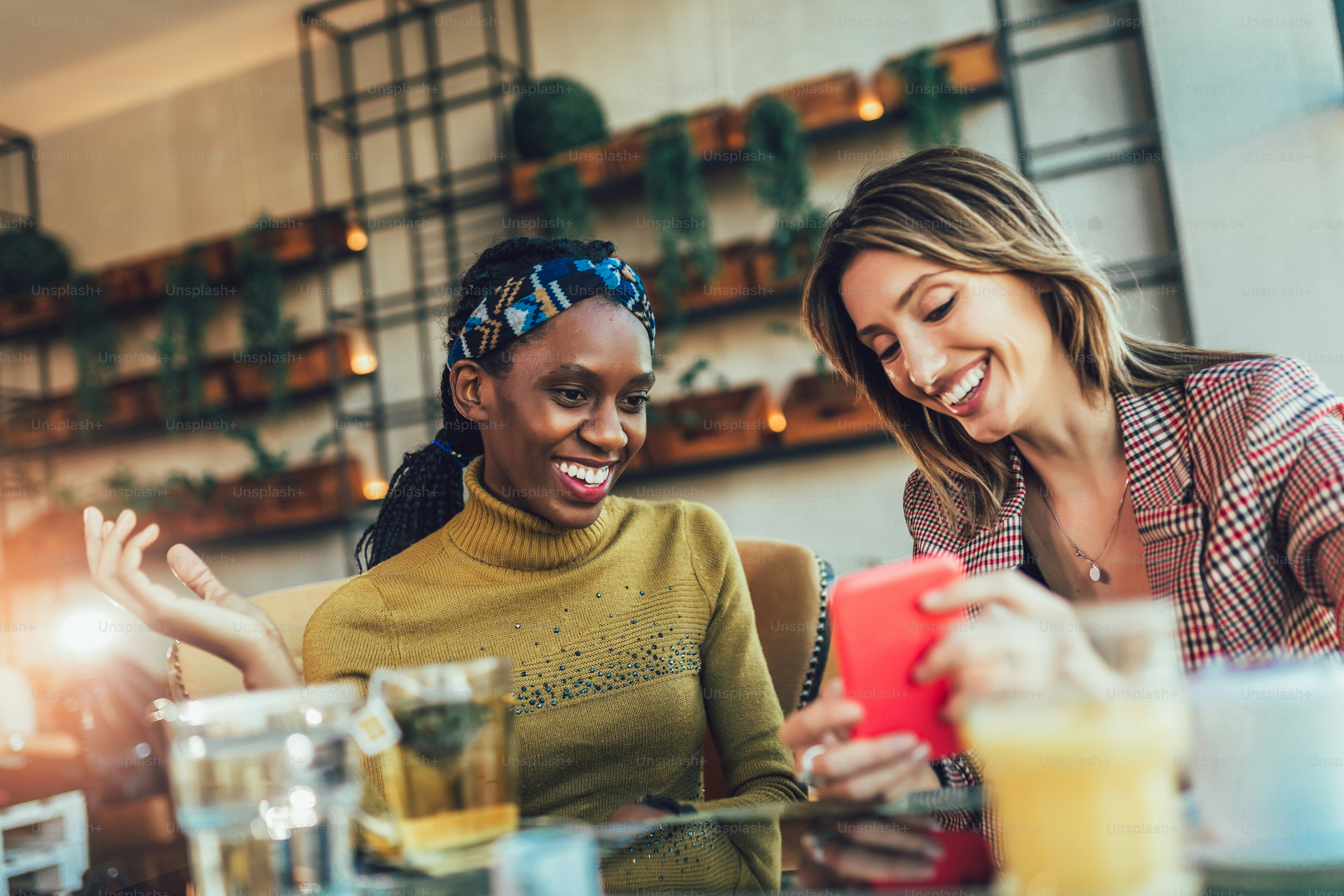 Two female friends talking at a coffee shop and using phone. photo ...