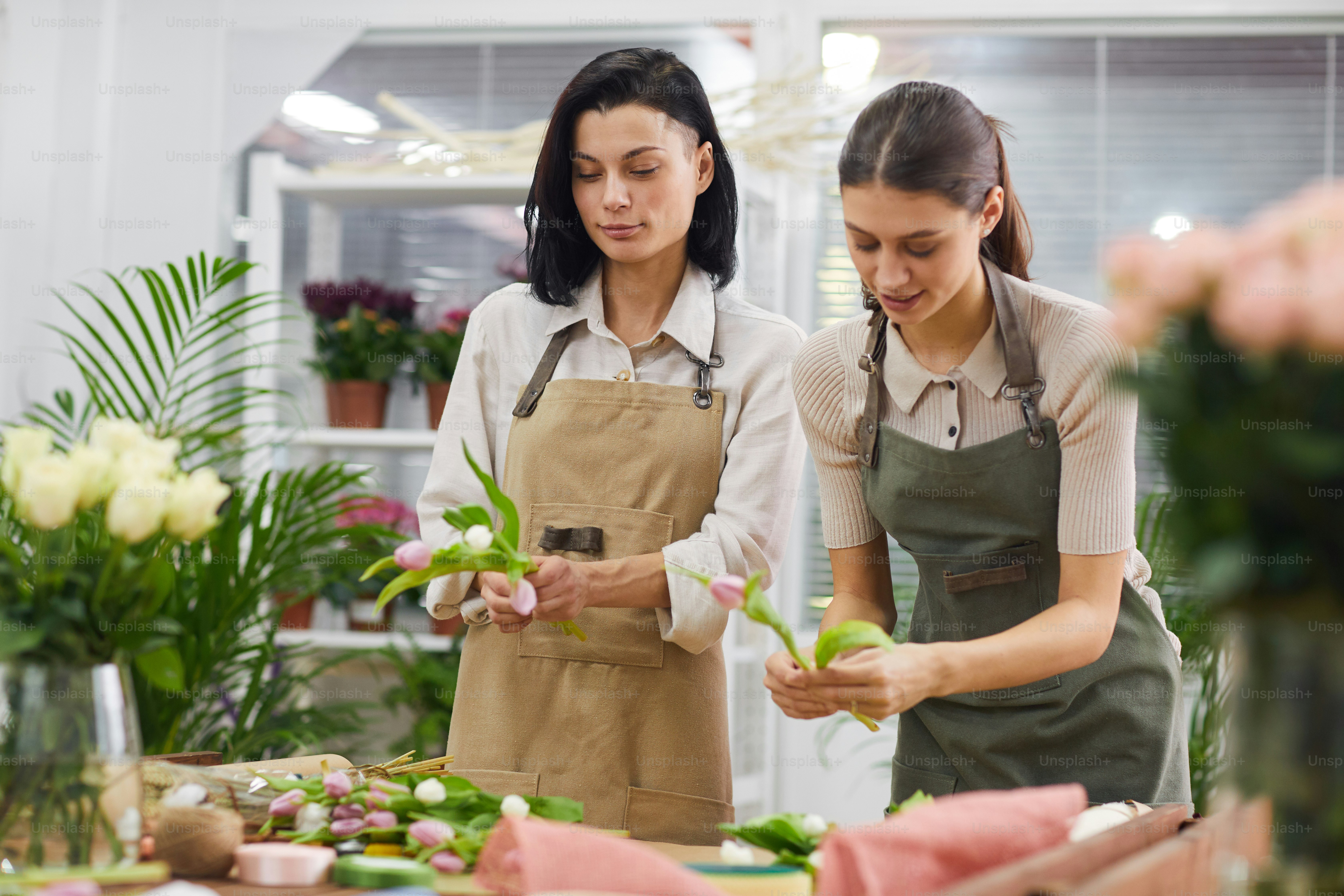 Waist up portrait of two young women arranging floral compositions and ...