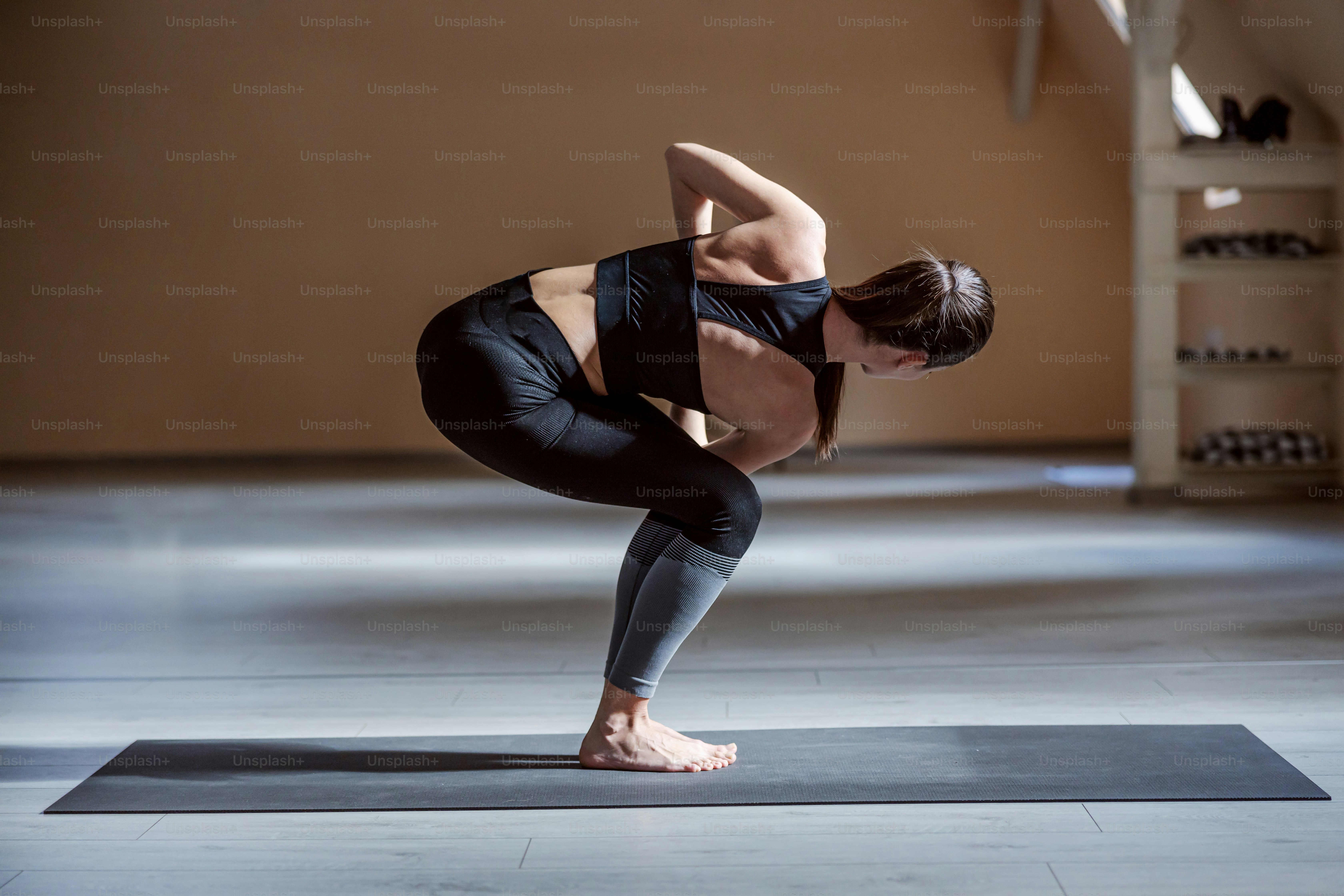 Beautiful brunette in active wear standing in Revolved Chair posture ...
