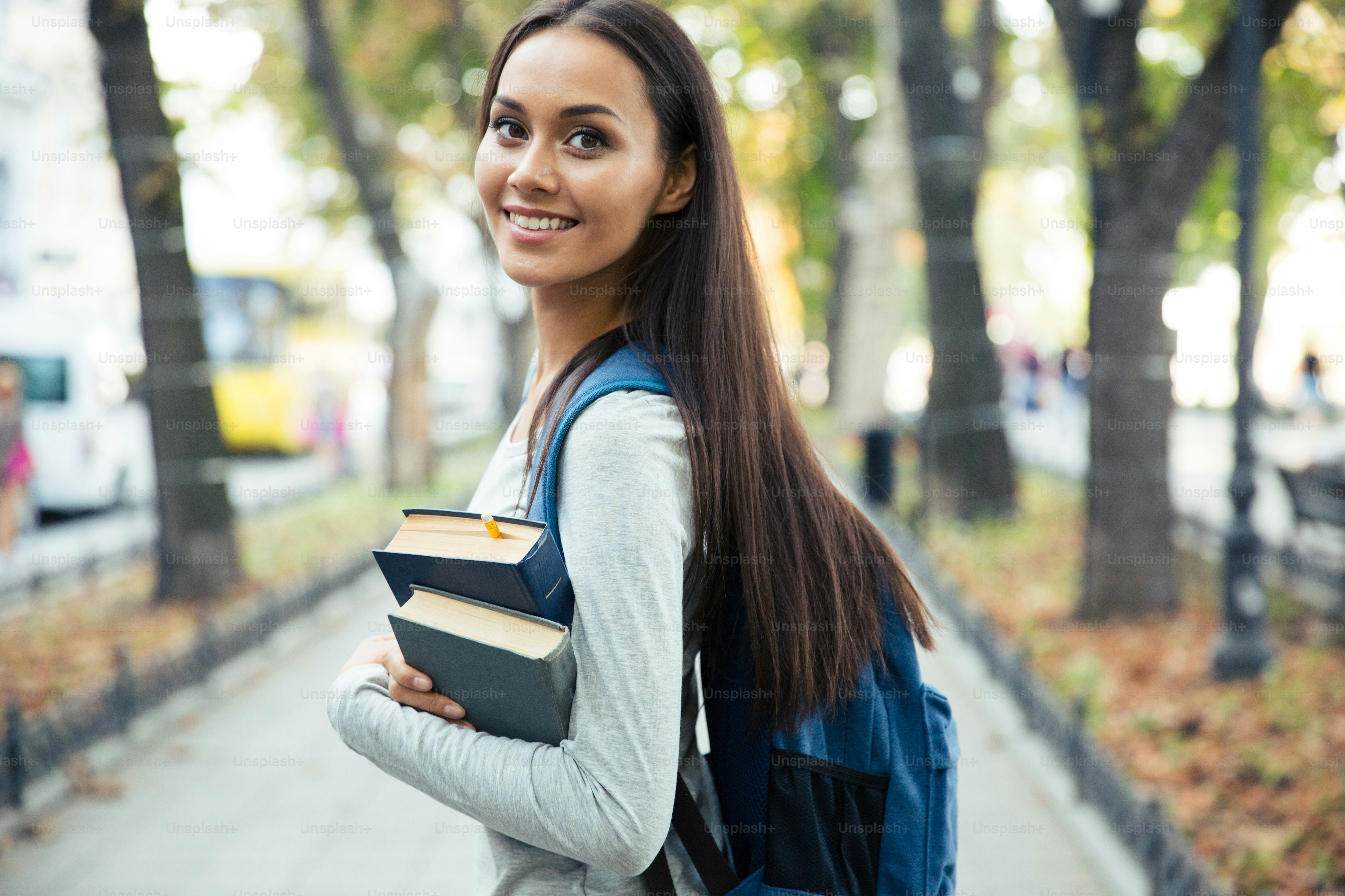 Portrait of a happy female student holding books and looking at camera ...