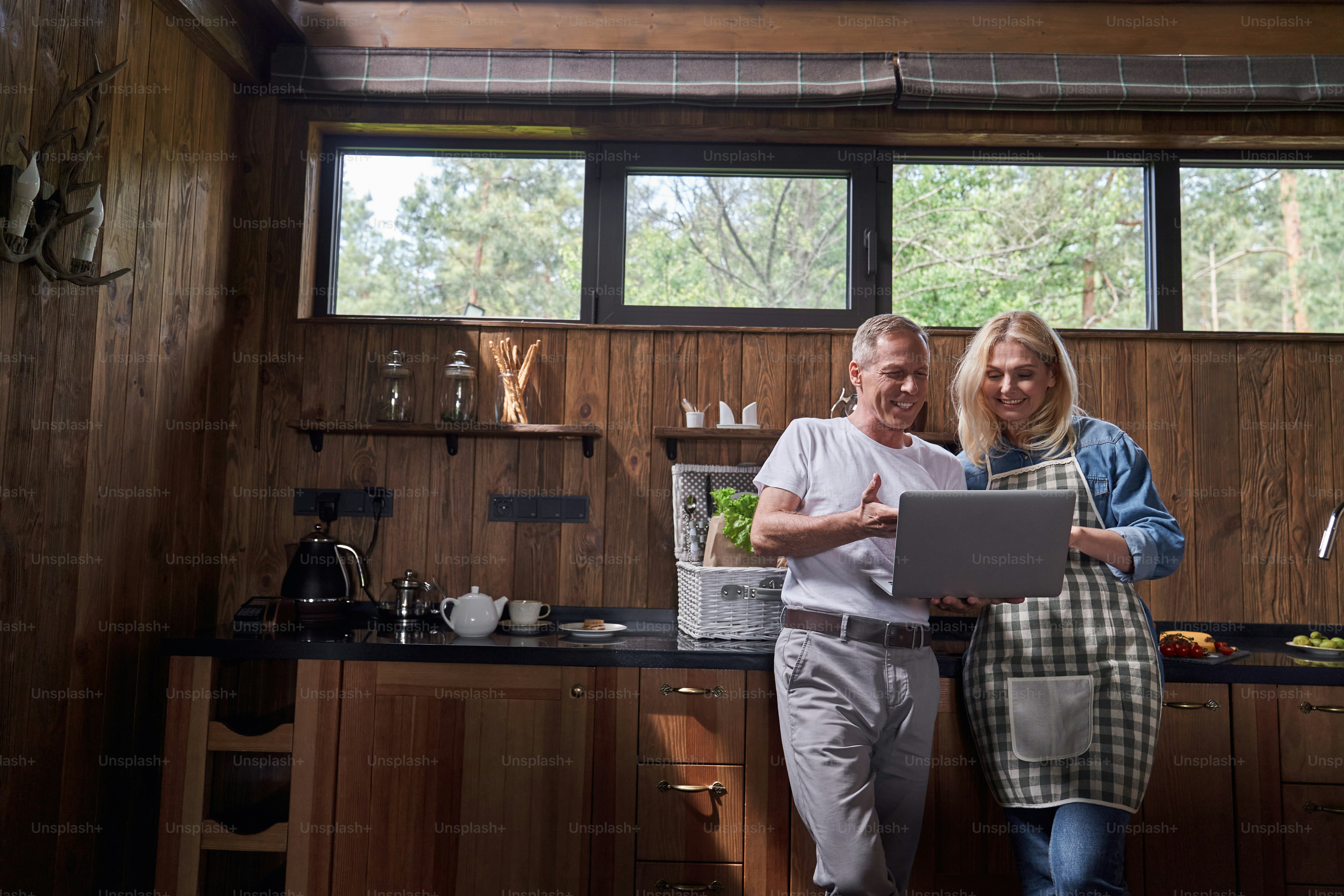 Jolly man and woman are standing indoors and looking at laptop screen ...
