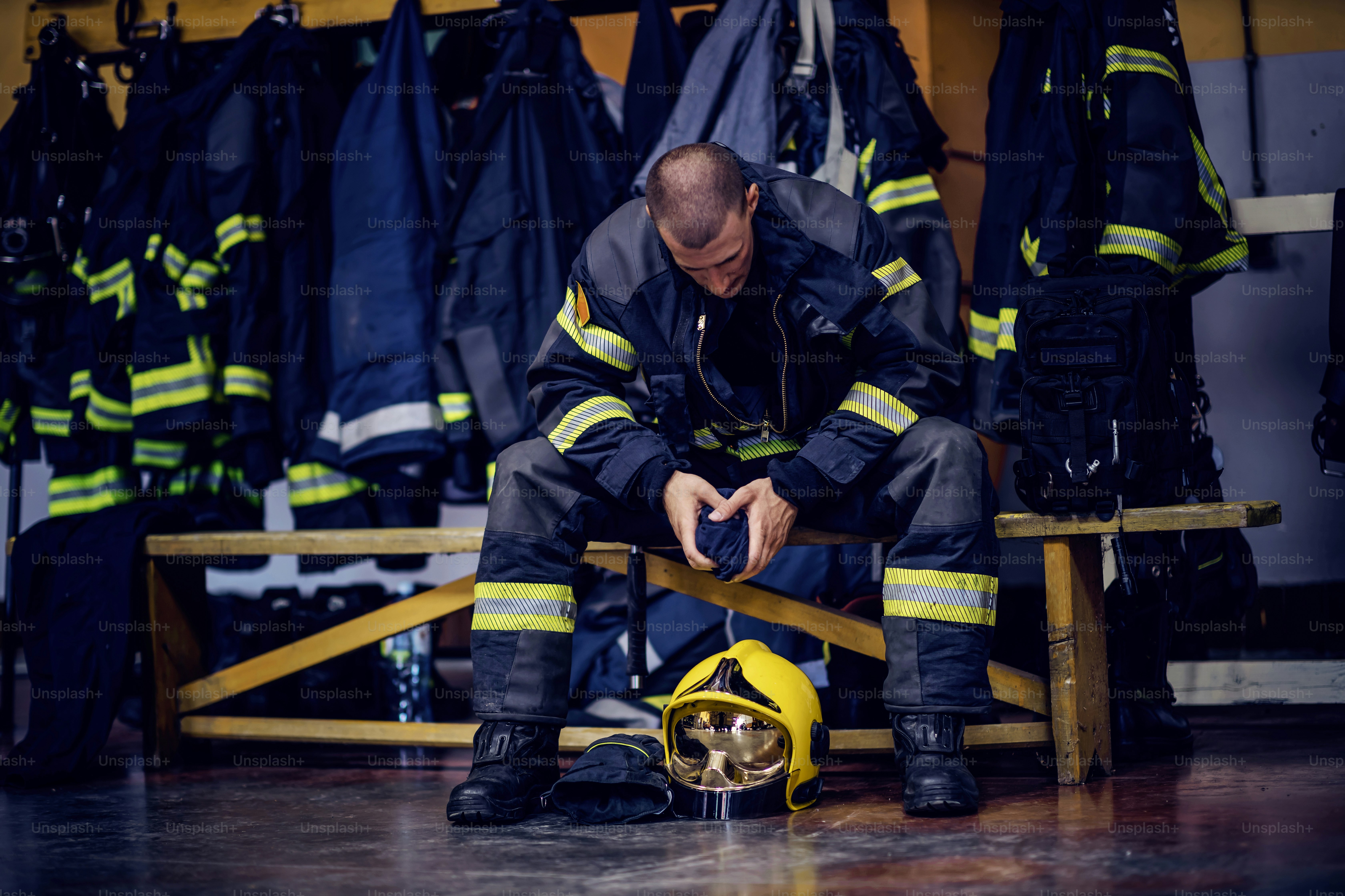 Young attractive fireman in protective uniform sitting in fire station ...