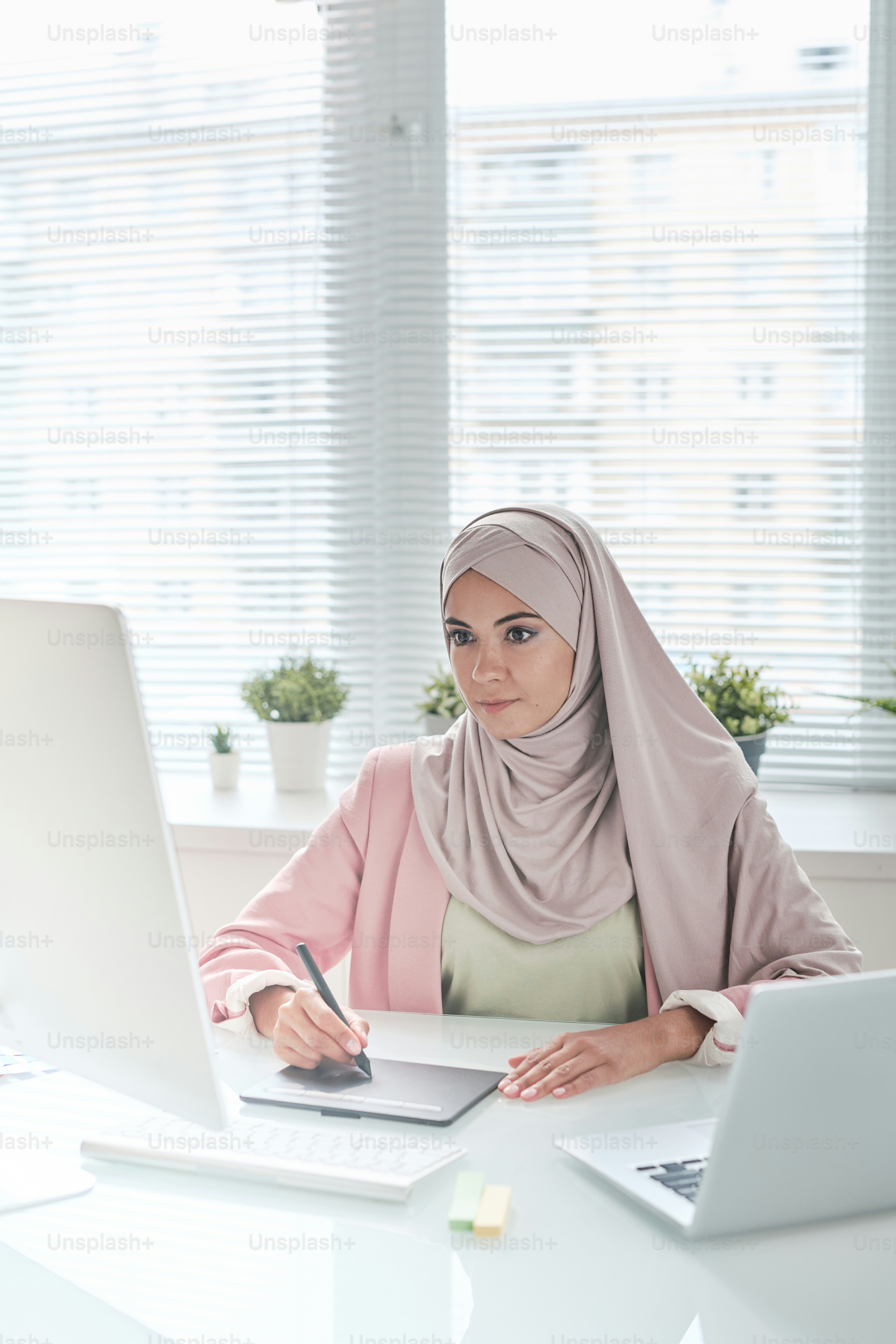 Busy young Muslim graphic designer in beautiful hijab sitting at desk ...