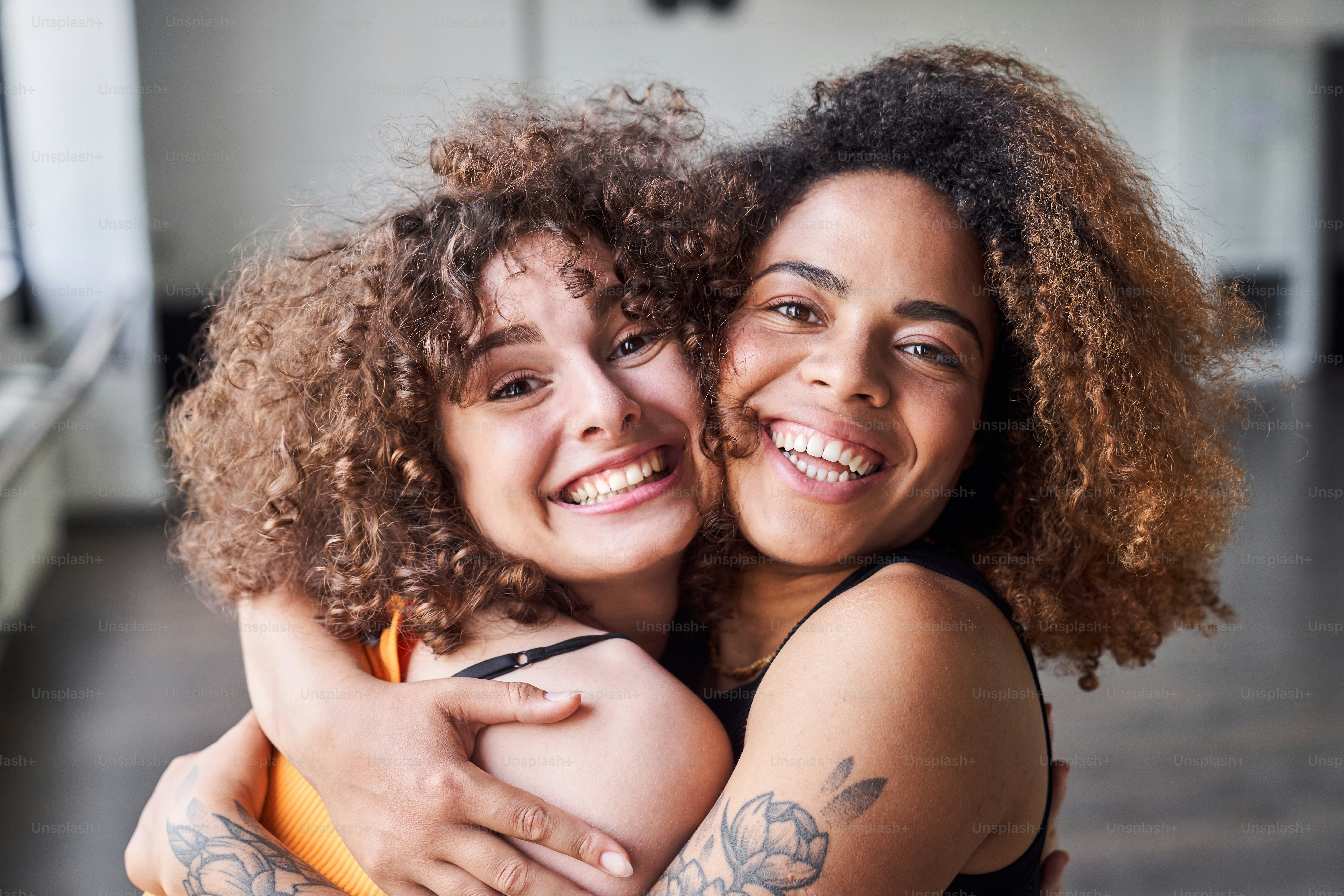 Waist up of happy pretty ladies hugging while looking at camera in ...