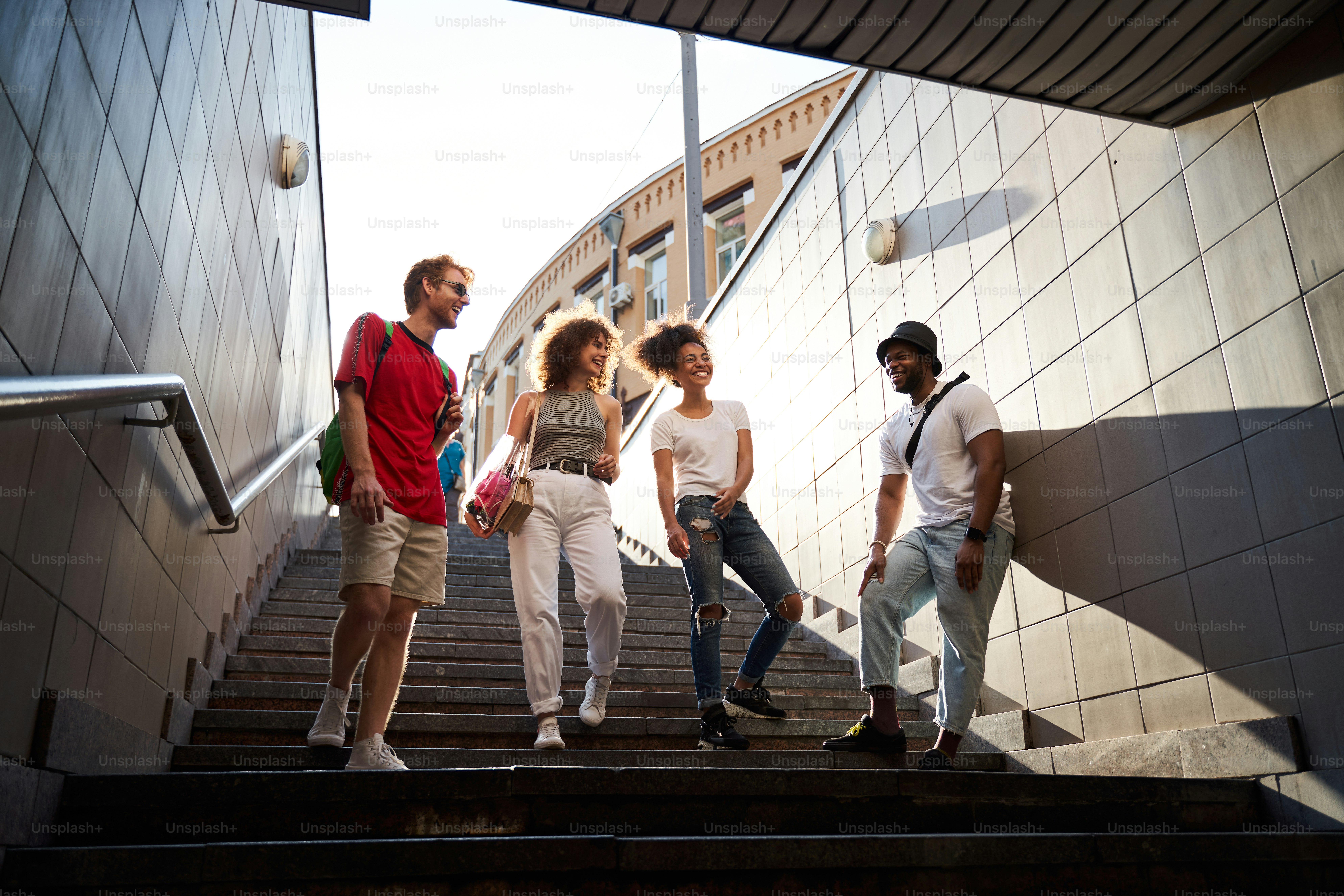 Low angle of jolly four friends walking downstairs into subway while ...