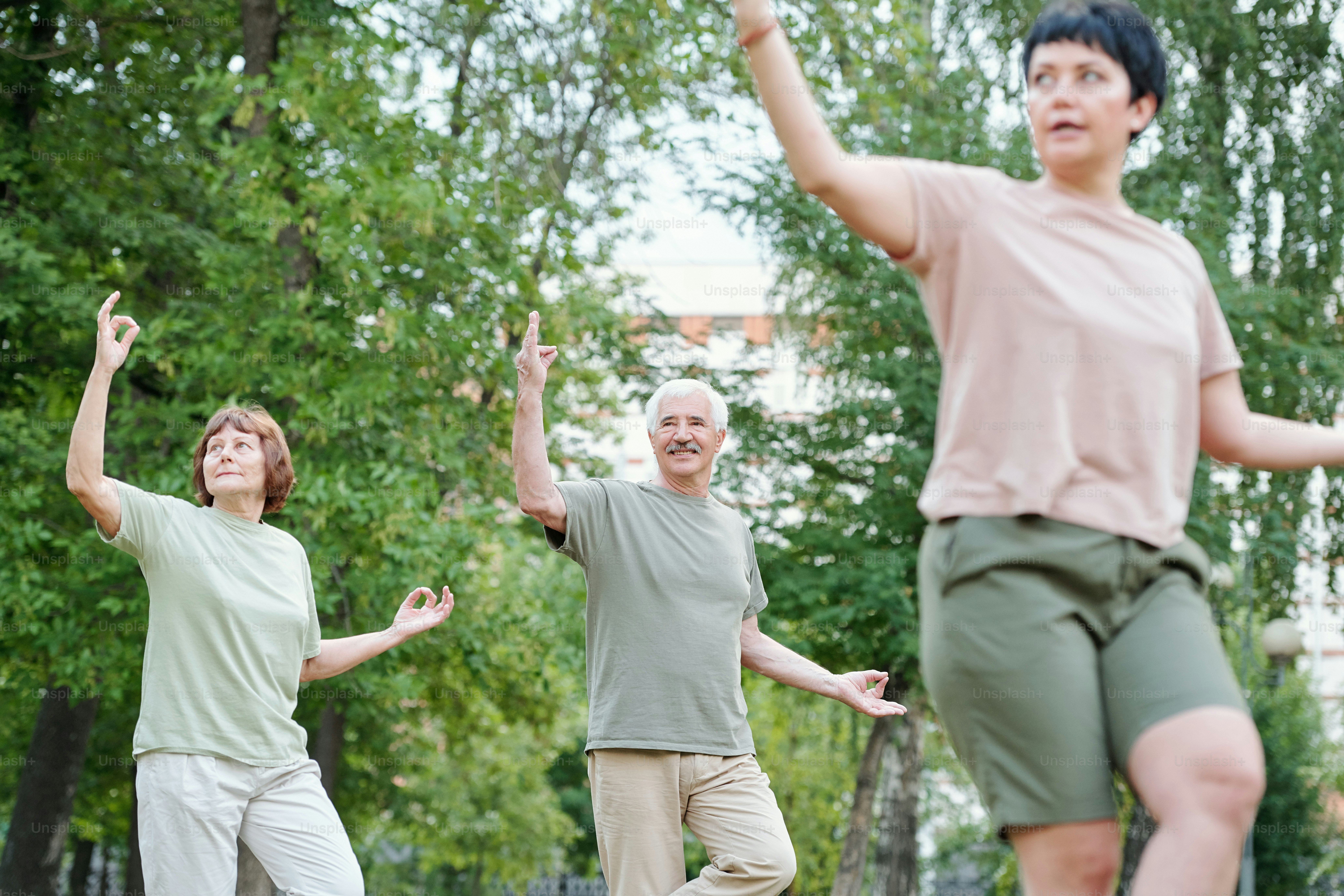 Content senior couple performing slow-flowing movements at group qigong ...