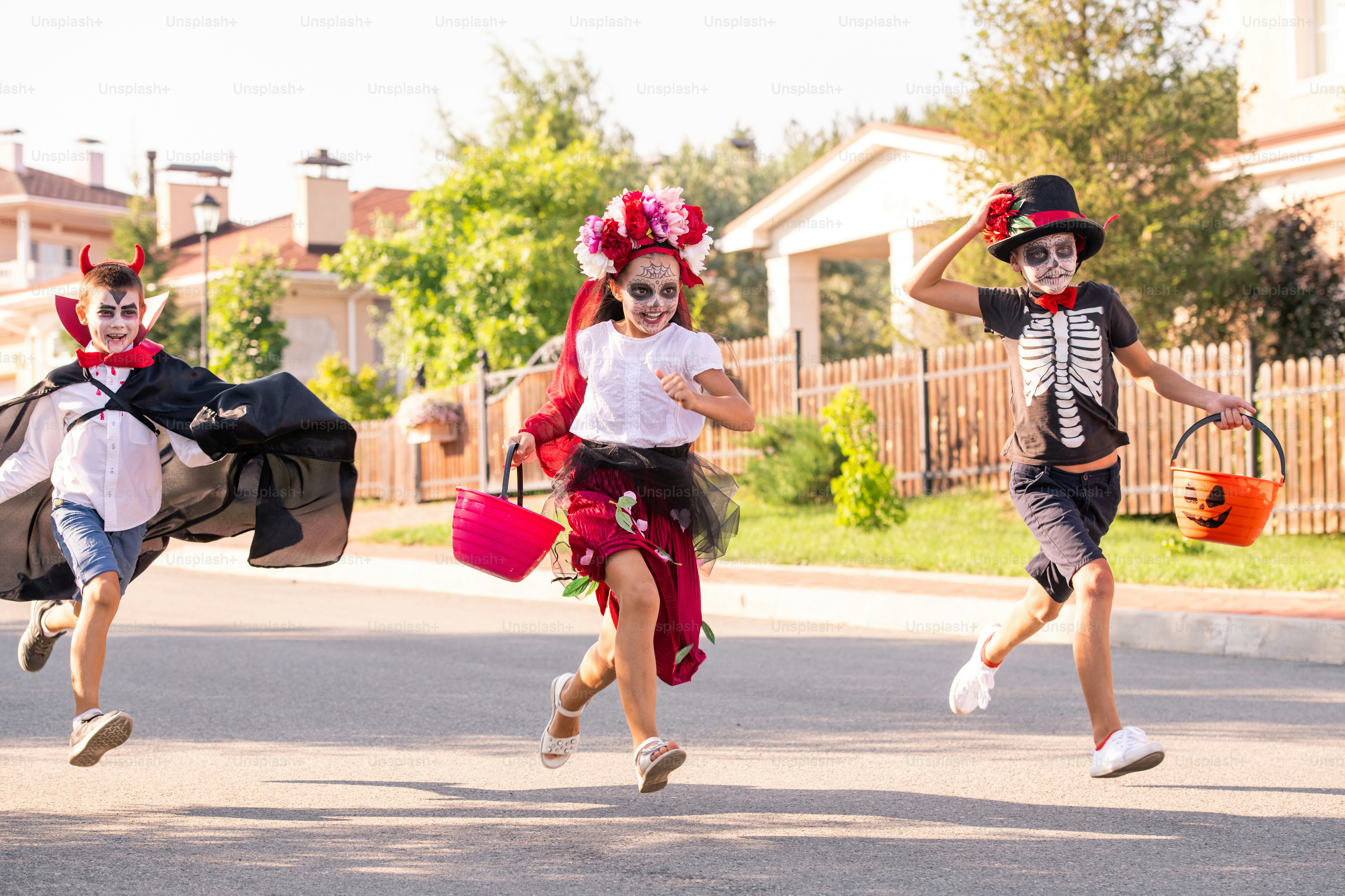 Three laughing kids in halloween costumes running down wide road on ...