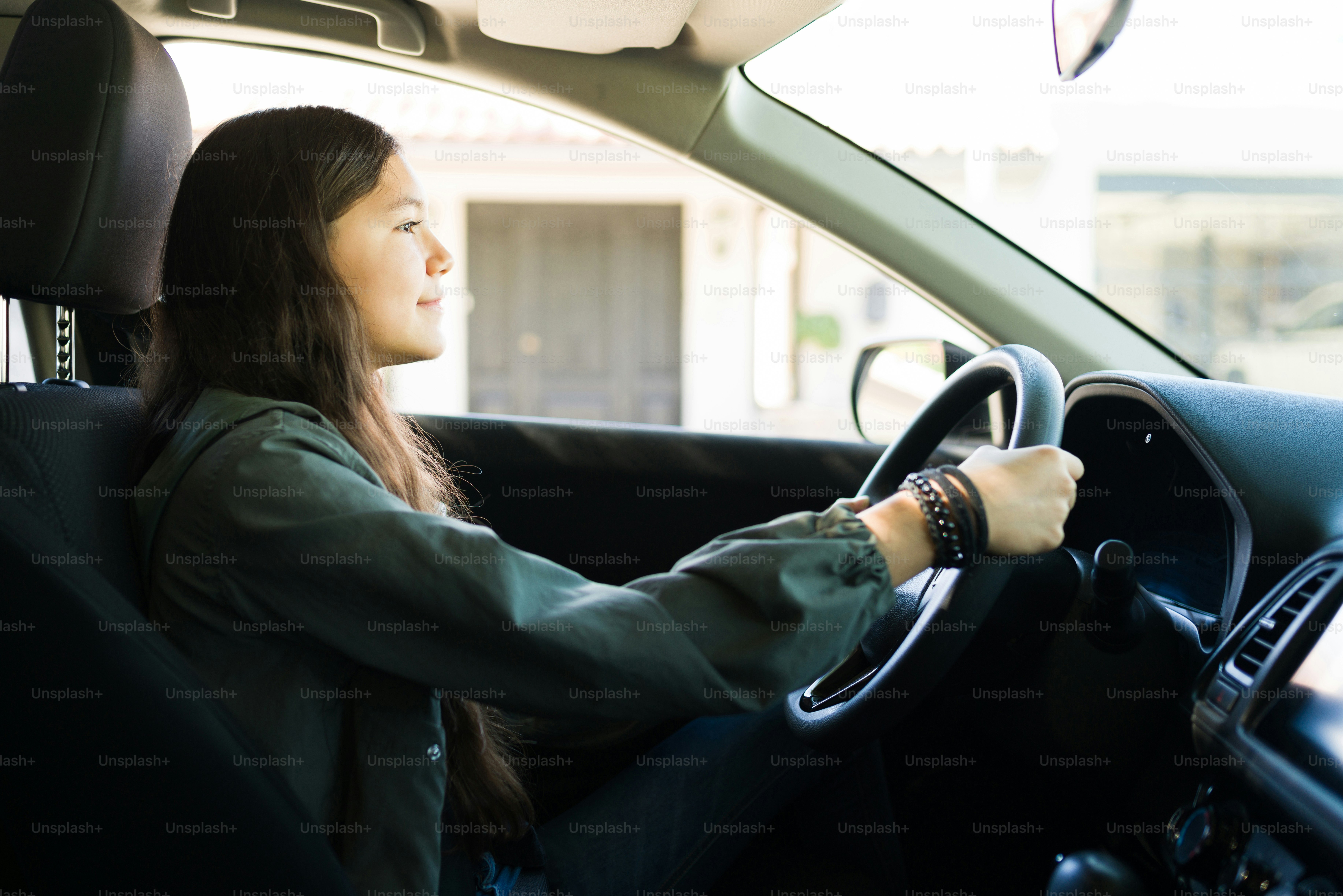 Cheerful teen girl driving her car alone during the day and practicing ...