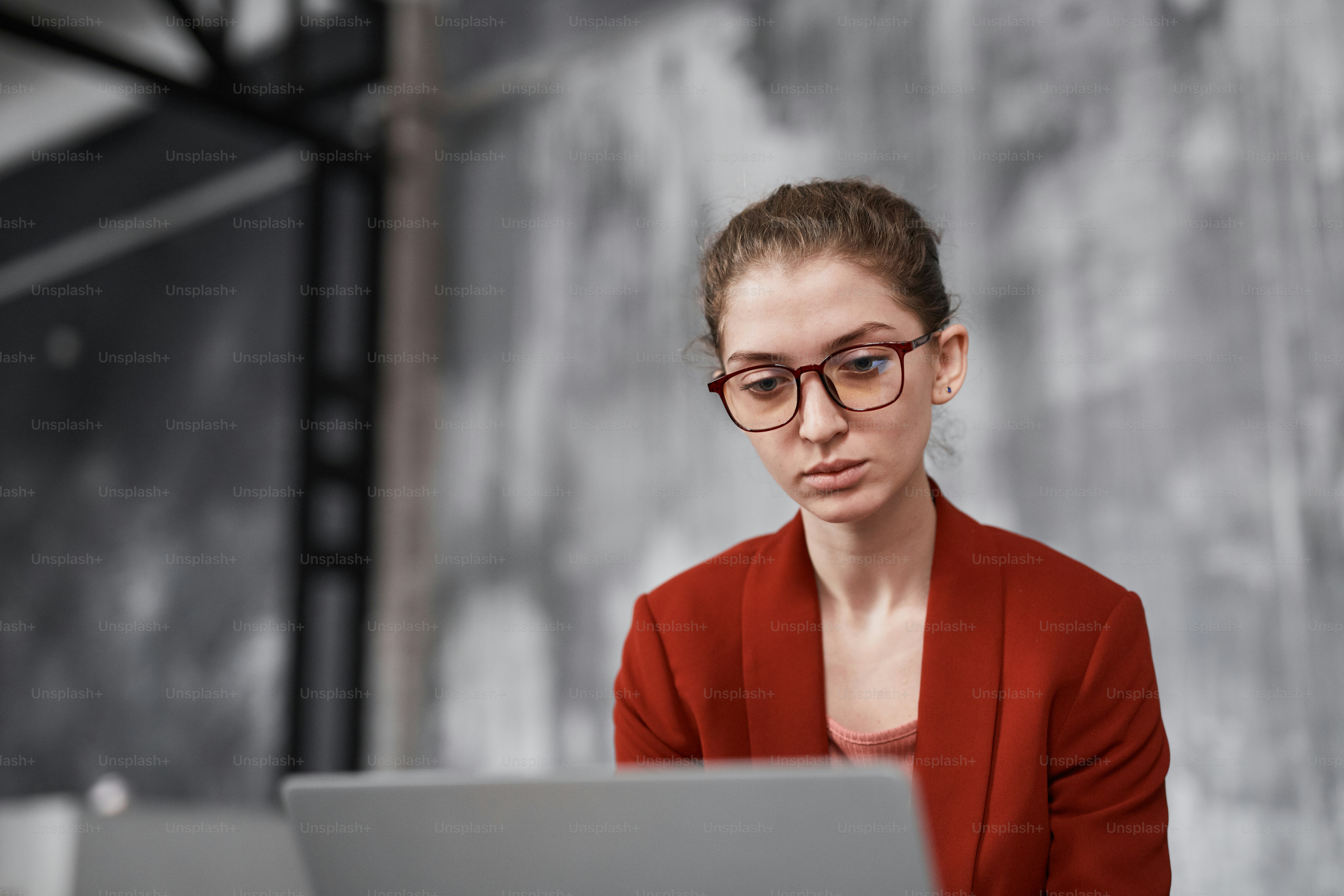 Portrait of young businesswoman wearing red while standing against grey ...