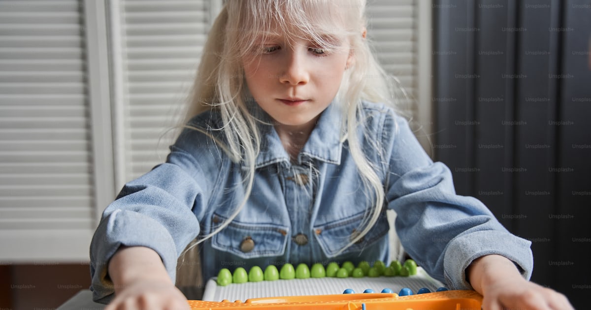 とても面白い。テーブルで折りたたんでゲームの詳細を見ている小さなアルビノの女の子の腰のポートレートビュー。レジャーゲームのコンセプトの写真