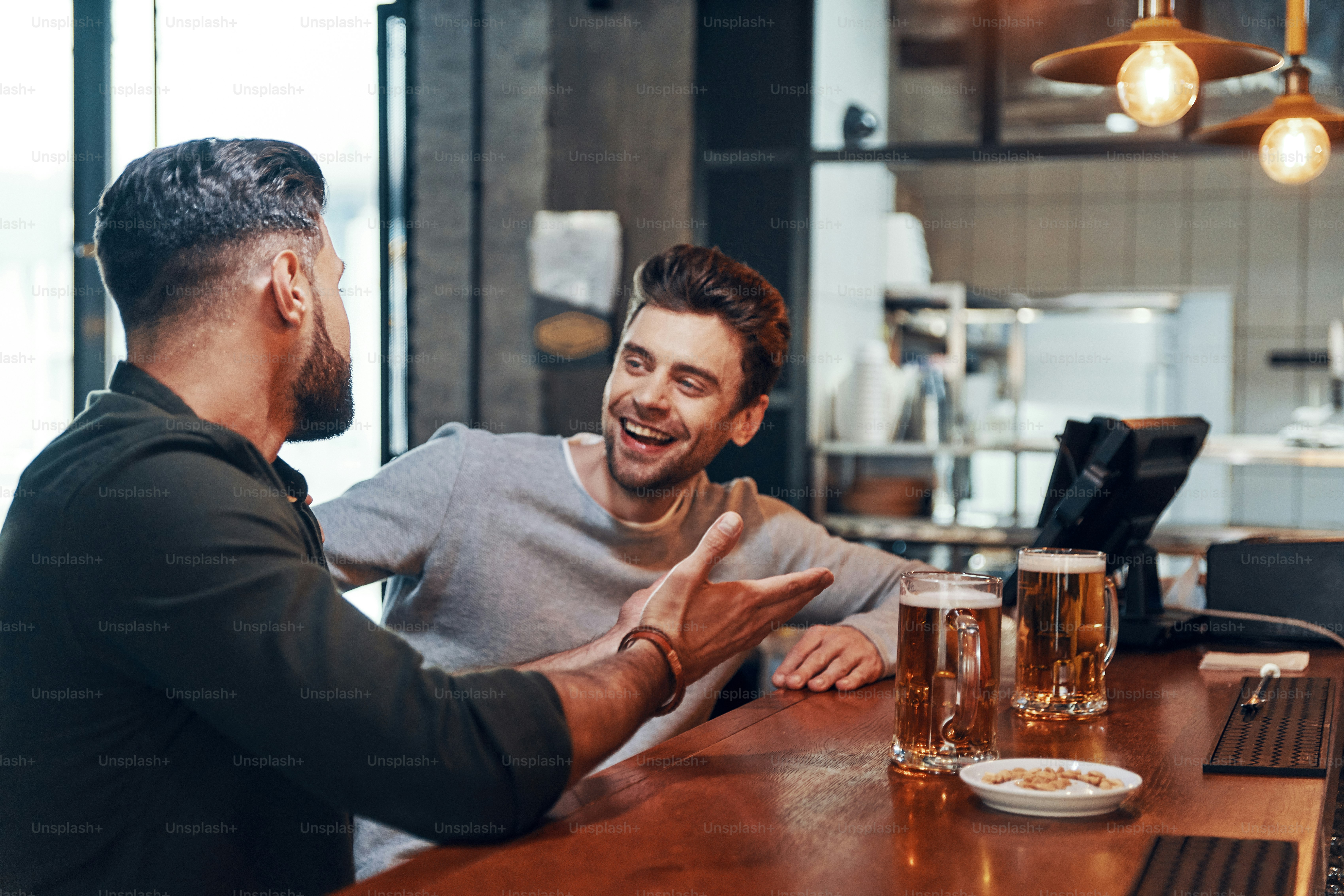Cheerful bartender serving beer to young men while standing at the bar ...
