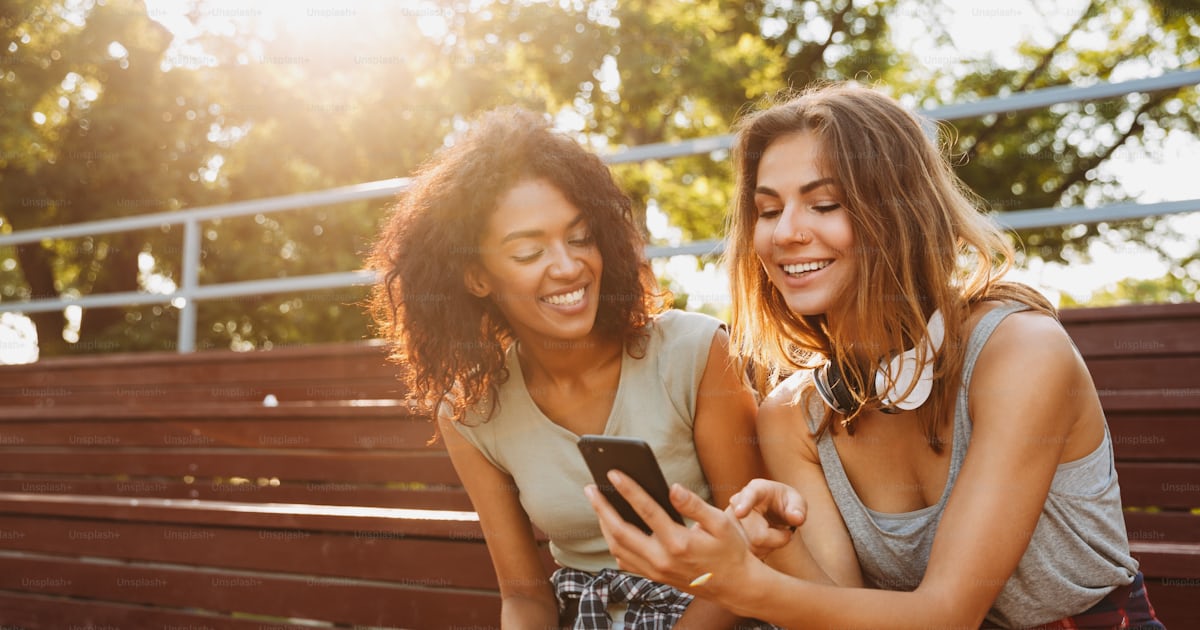 Deux Jeunes Filles Excitées Samusent Ensemble Tout En Utilisant Un Téléphone Portable Au Parc