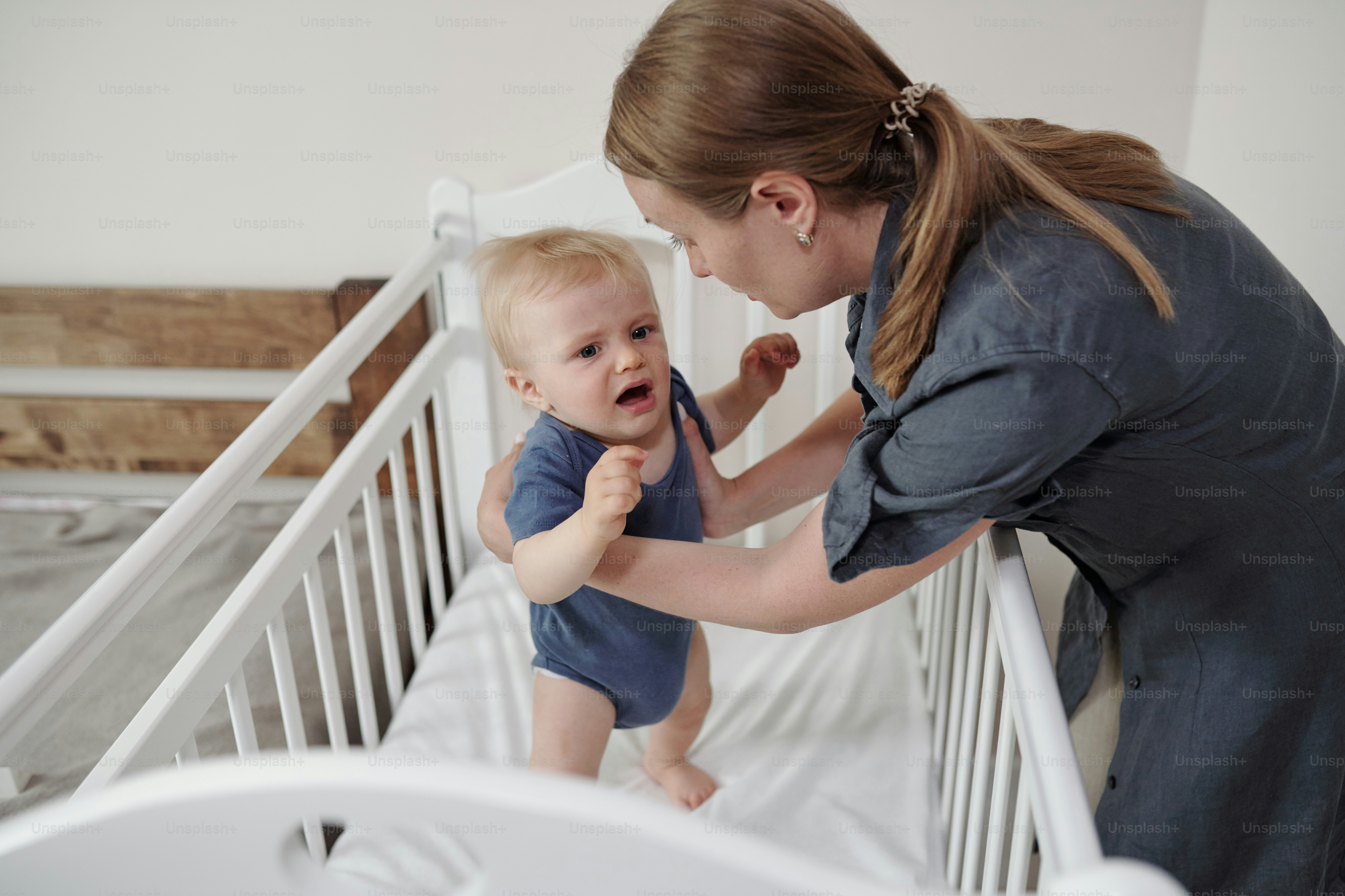 Young mother with ponytail taking frightened baby in arms from crib photo – Holding Image on ...