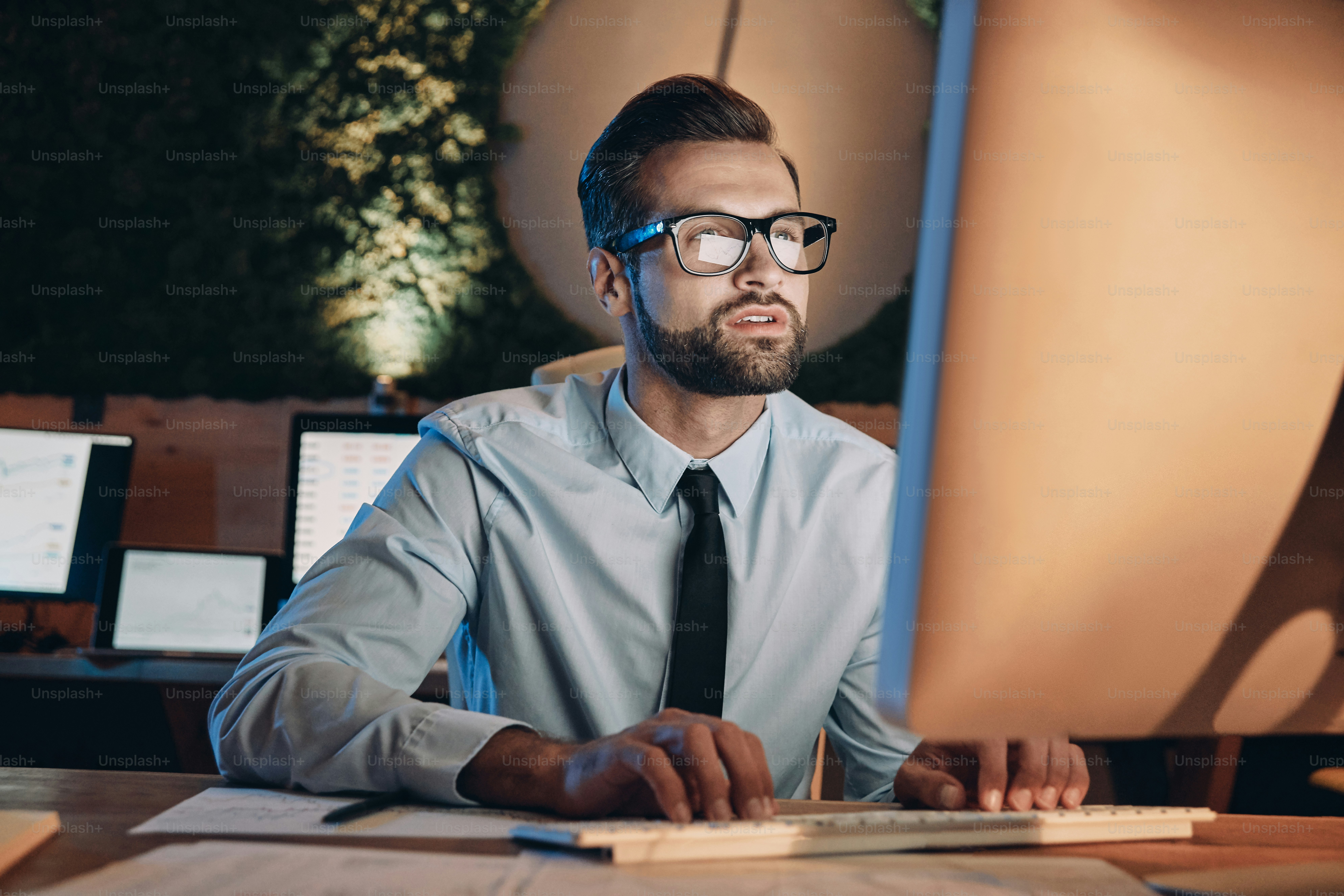 Confident young man working on computer while staying late in the ...
