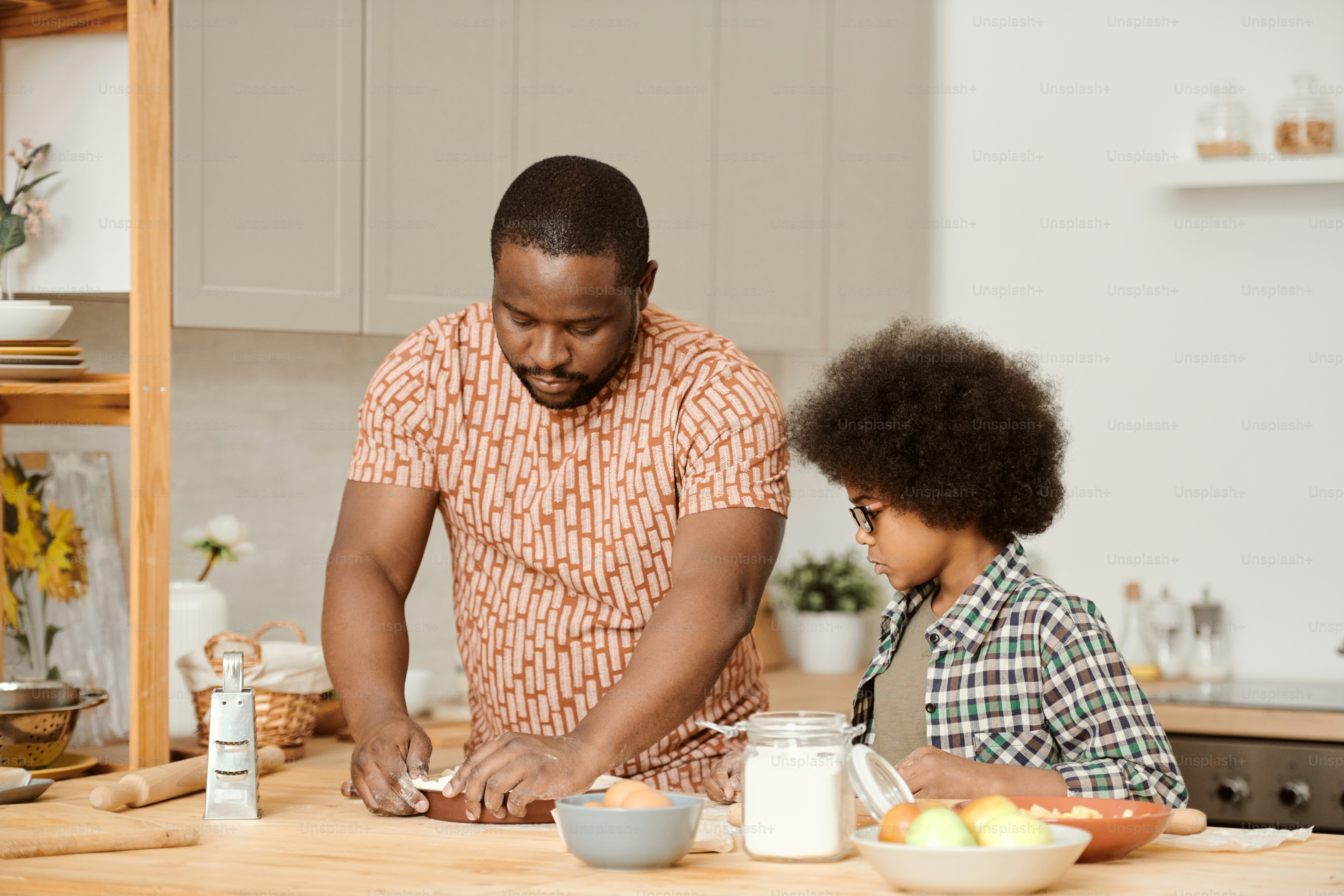 Cute little boy looking at his father putting dough in baking form ...