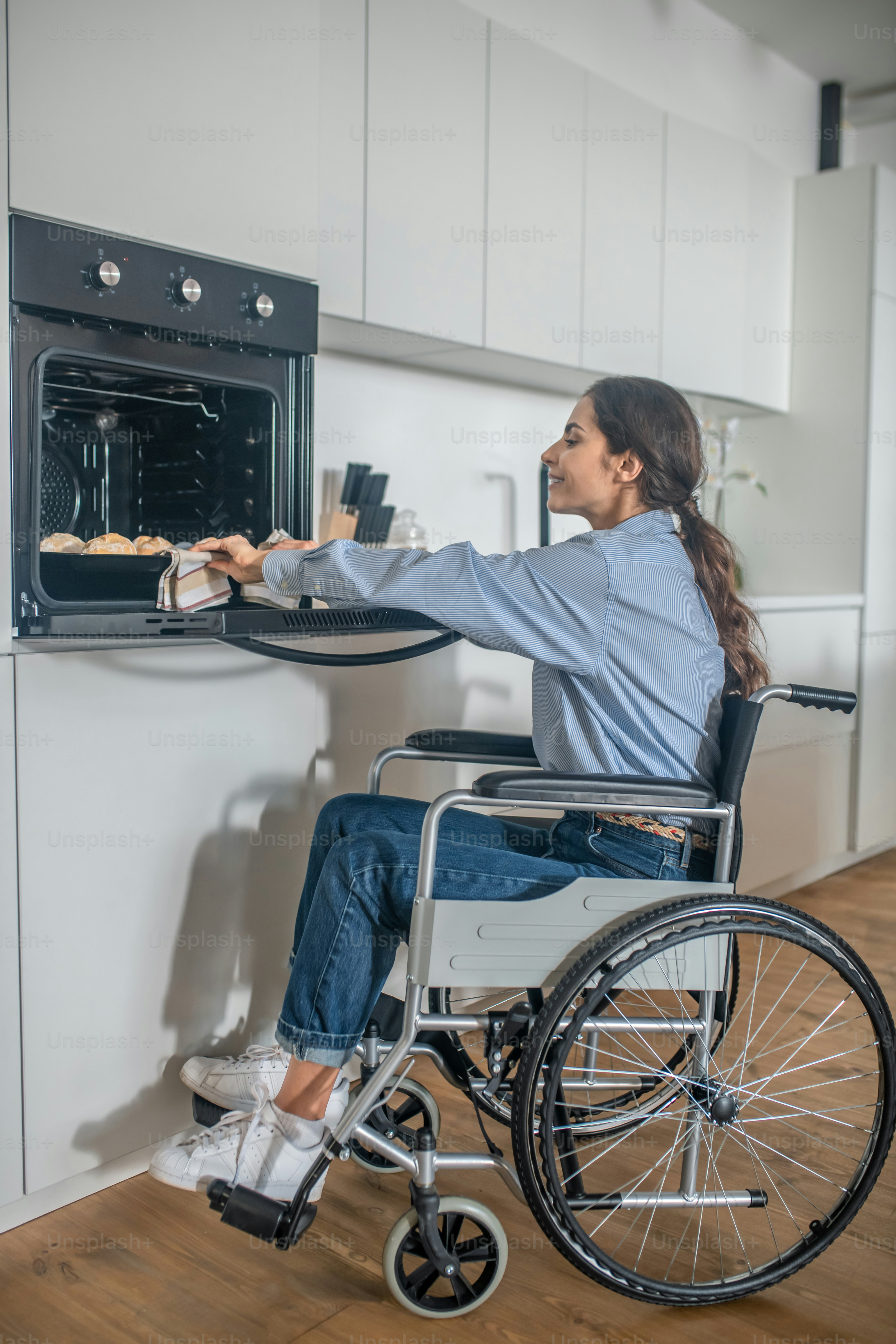 Cooking. A girl on a wheelchair opening oven in the kitchen while ...