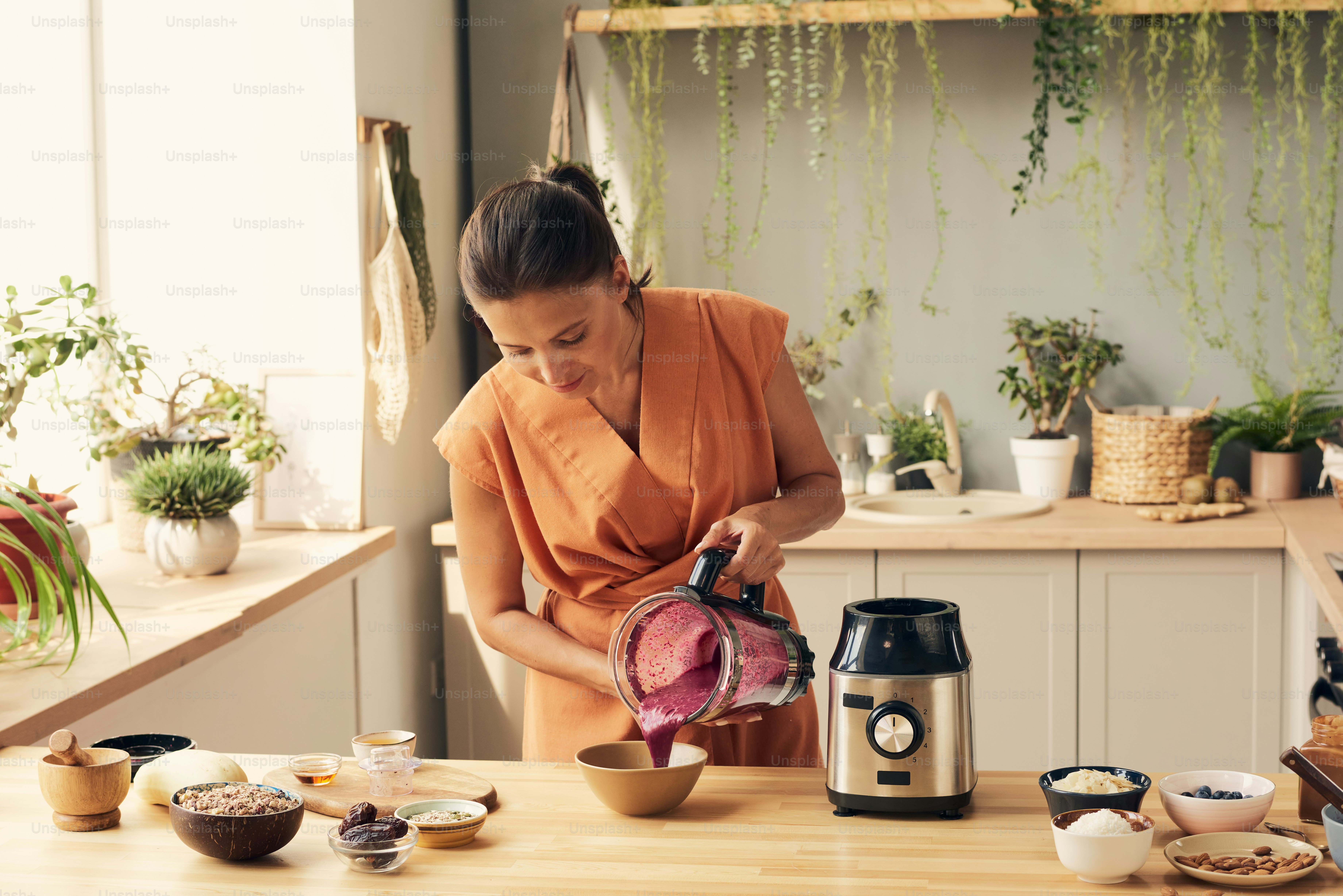 Young brunette woman bending over kitchen table while pouring fresh ...