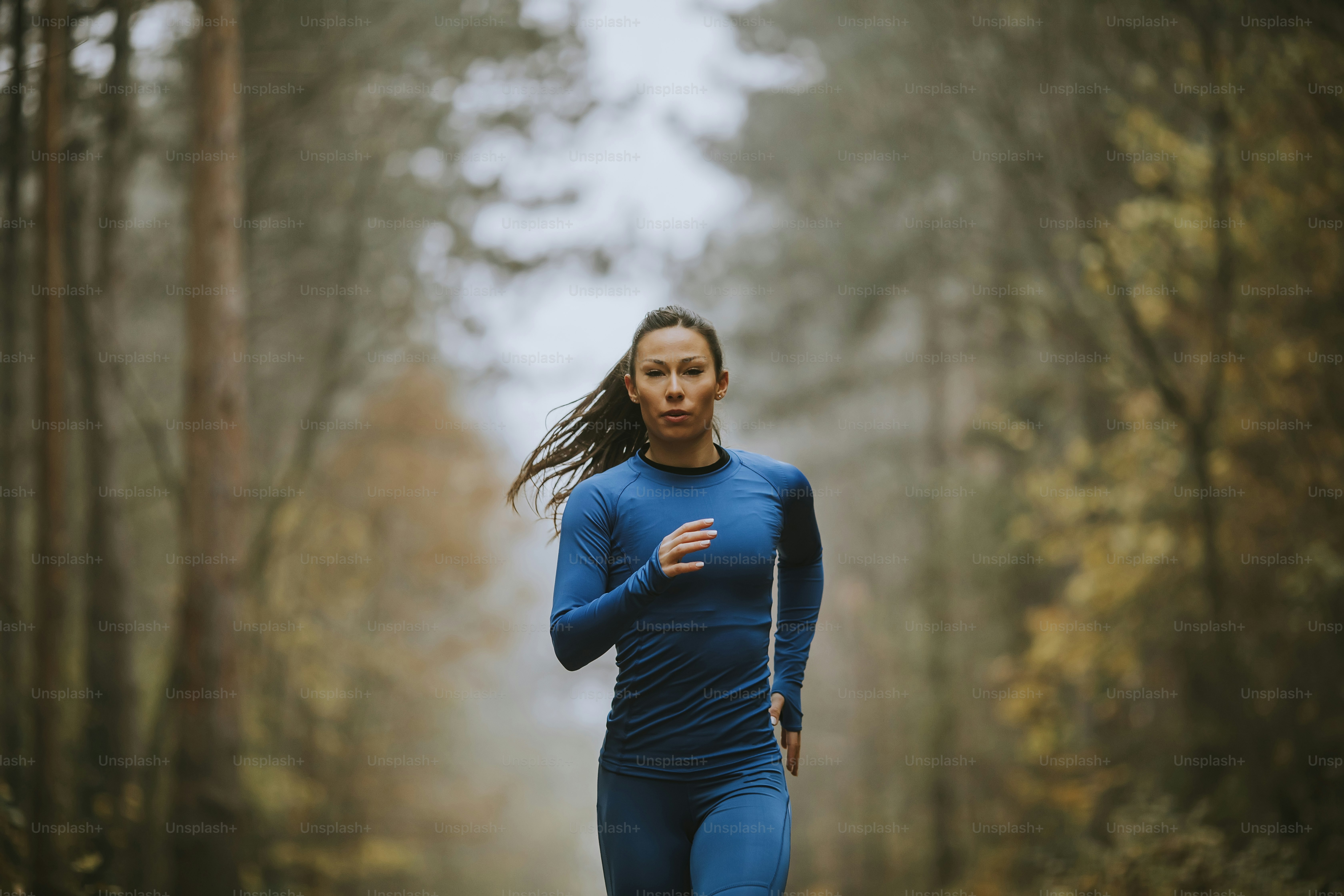 Pretty young woman in blue track suit running by the river at autumn ...