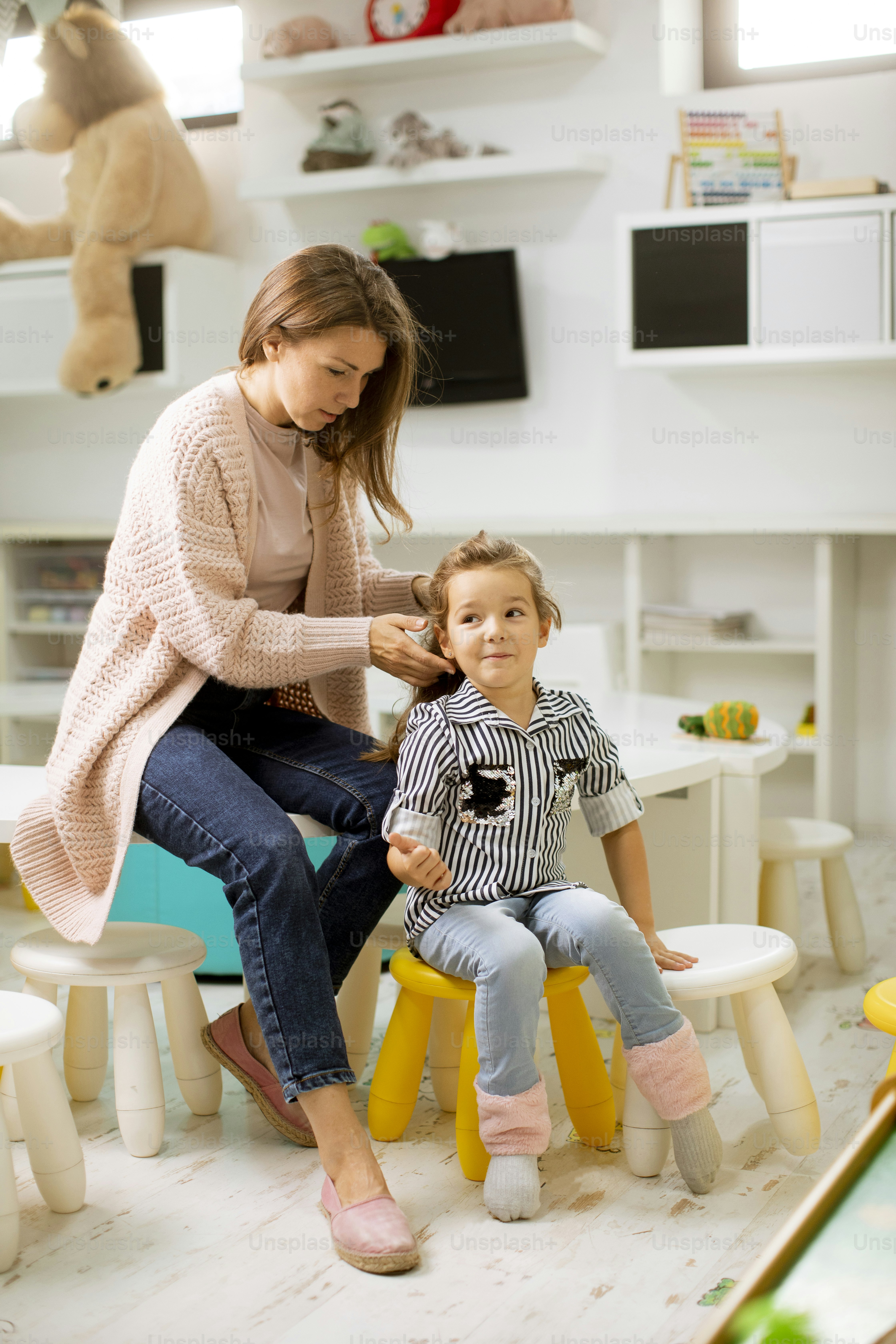 Nursery teacher helping cute little girl to fix hair in the ...