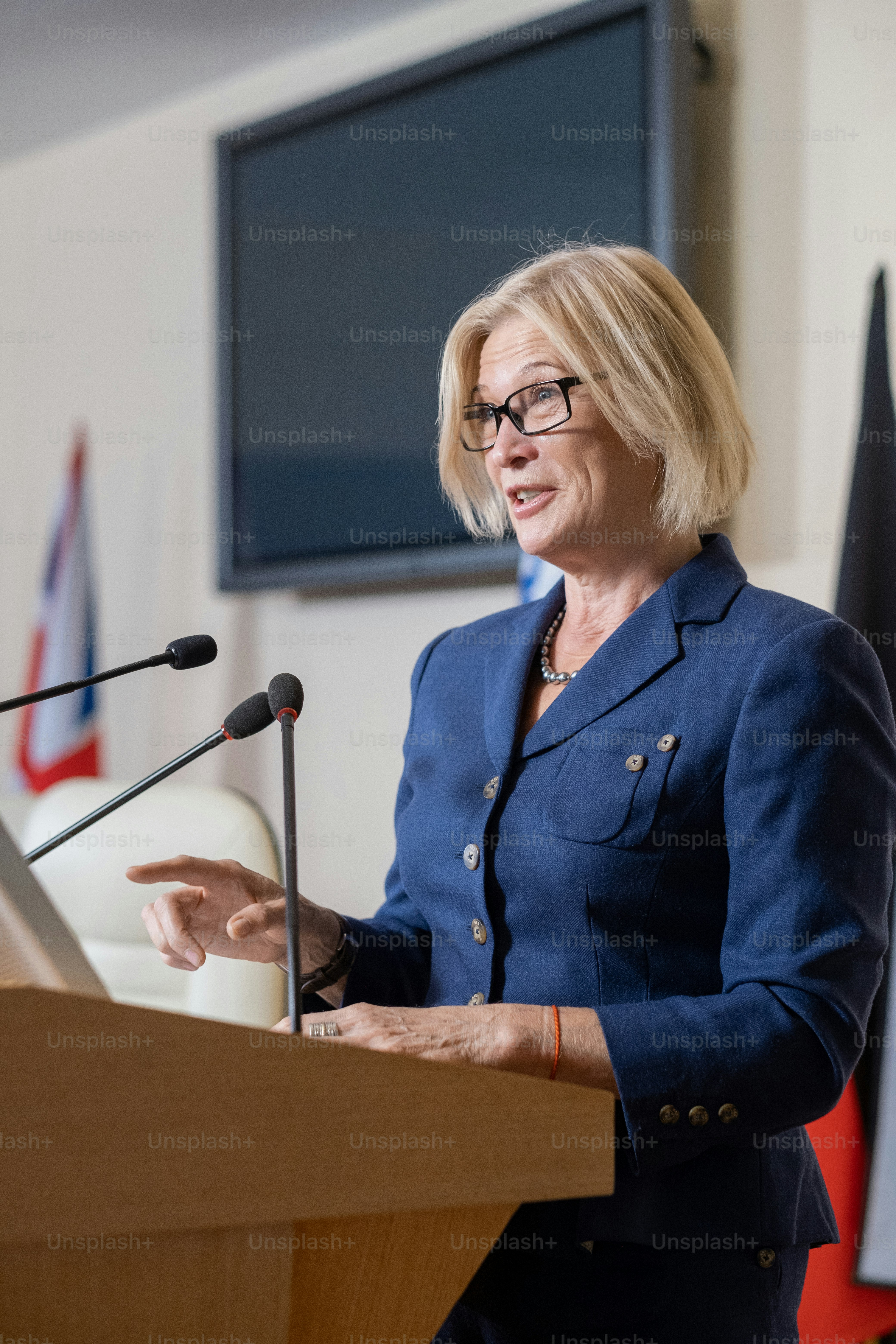 Mature female delegate standing by tribune at political conference and ...