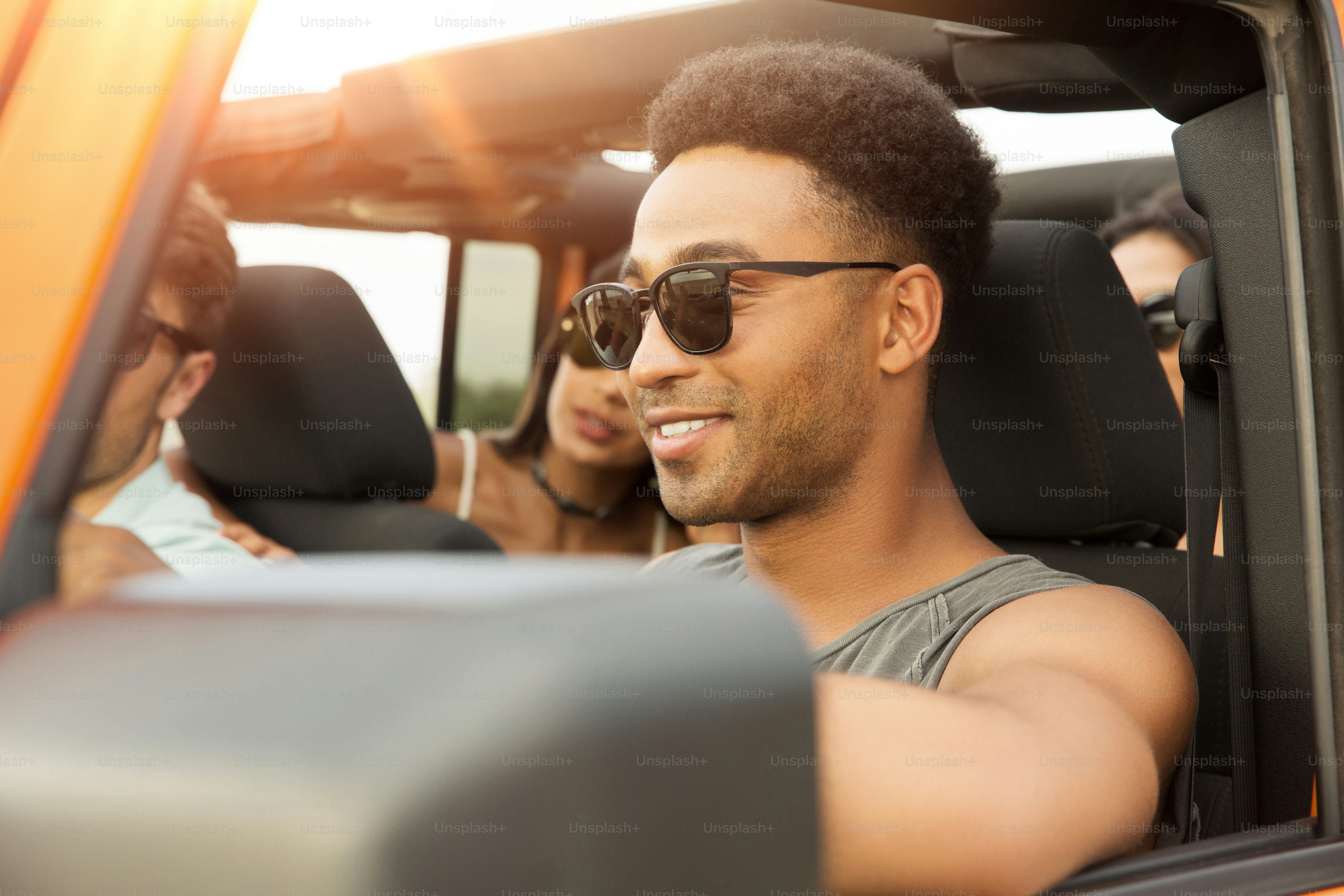 Smiling young african man driving a car and having fun with his friends ...
