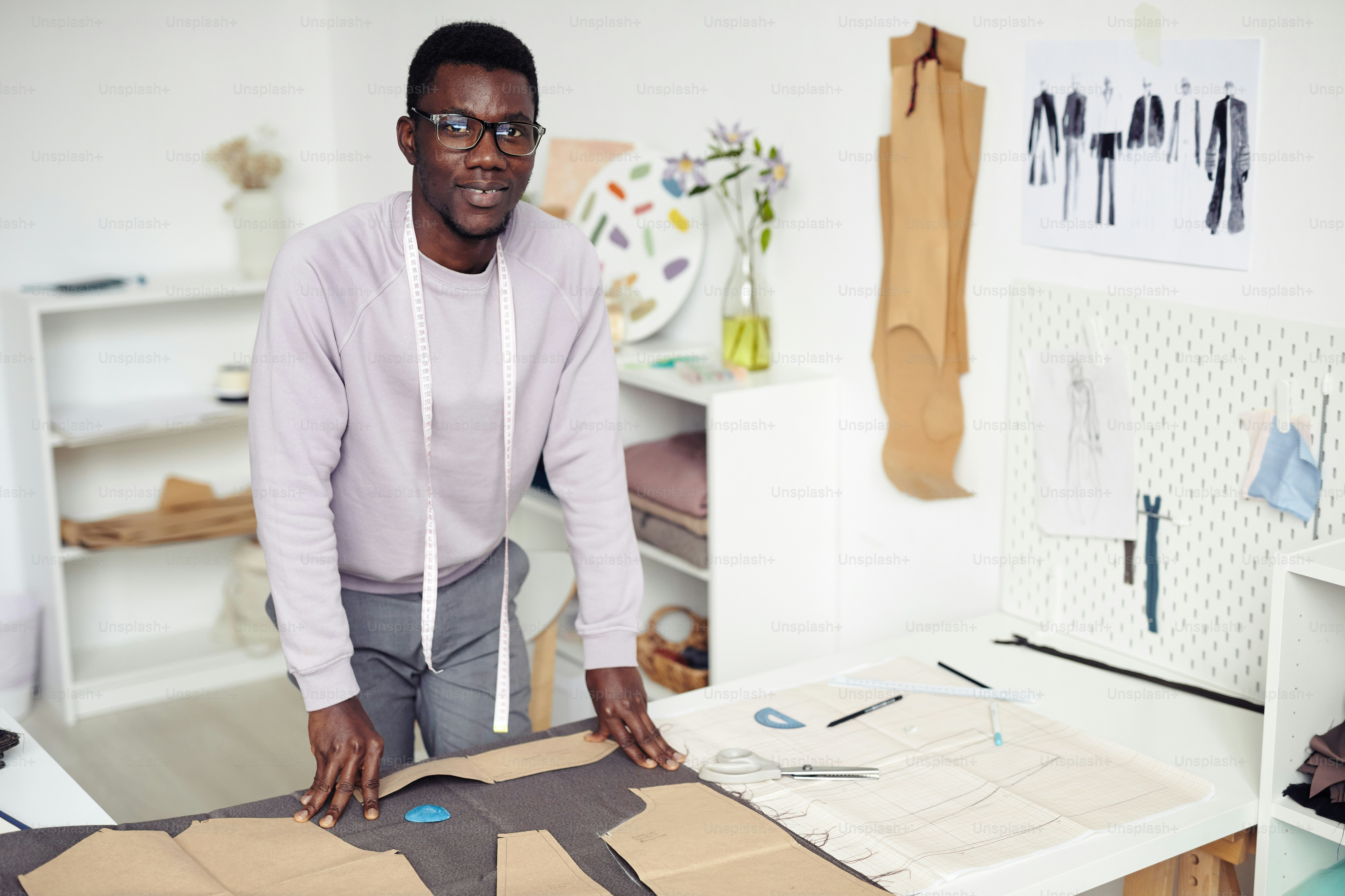 Portrait of young smiling African American tailor leaning on table with ...