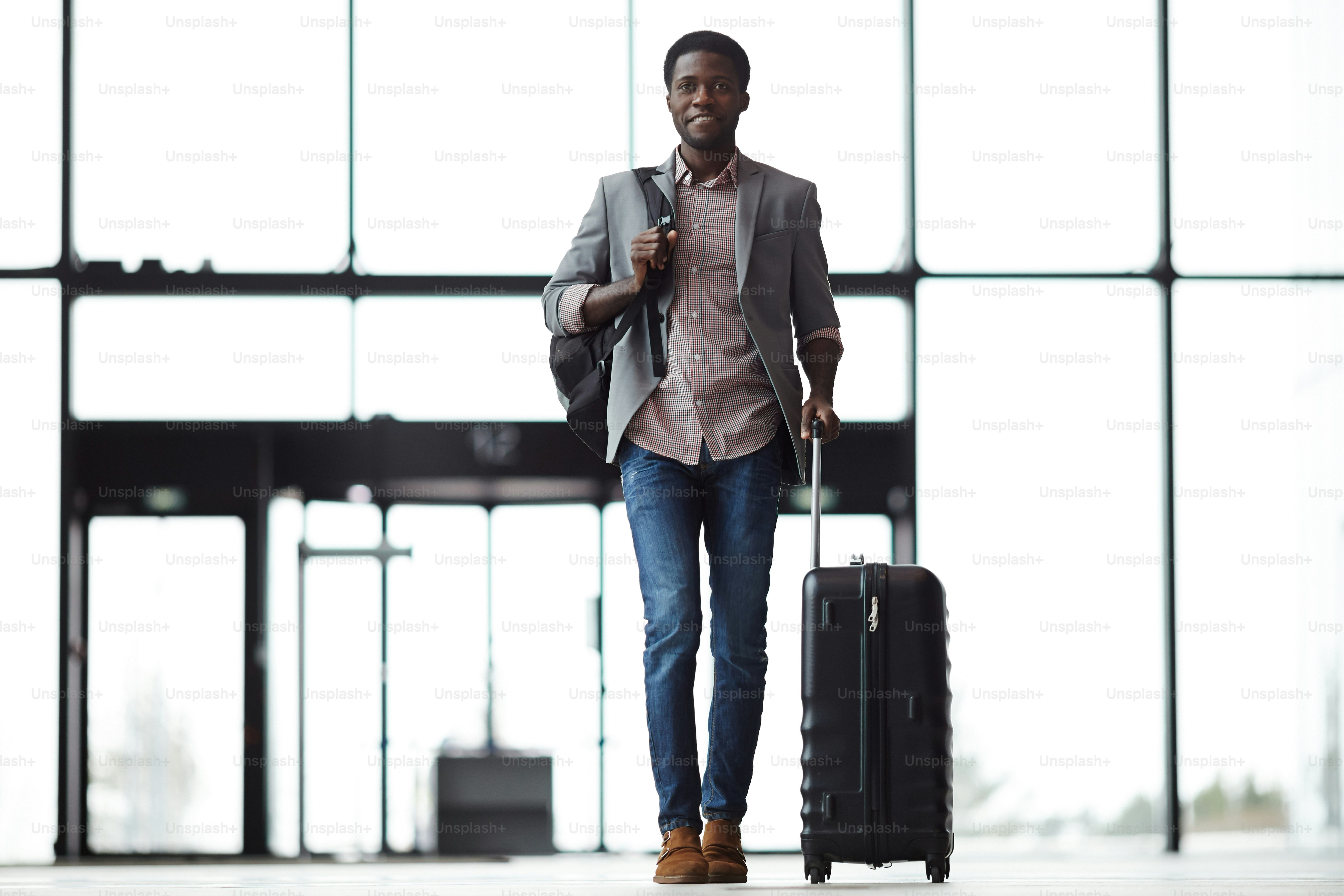 Happy young man with backpack and suitcase walking along airport to ...