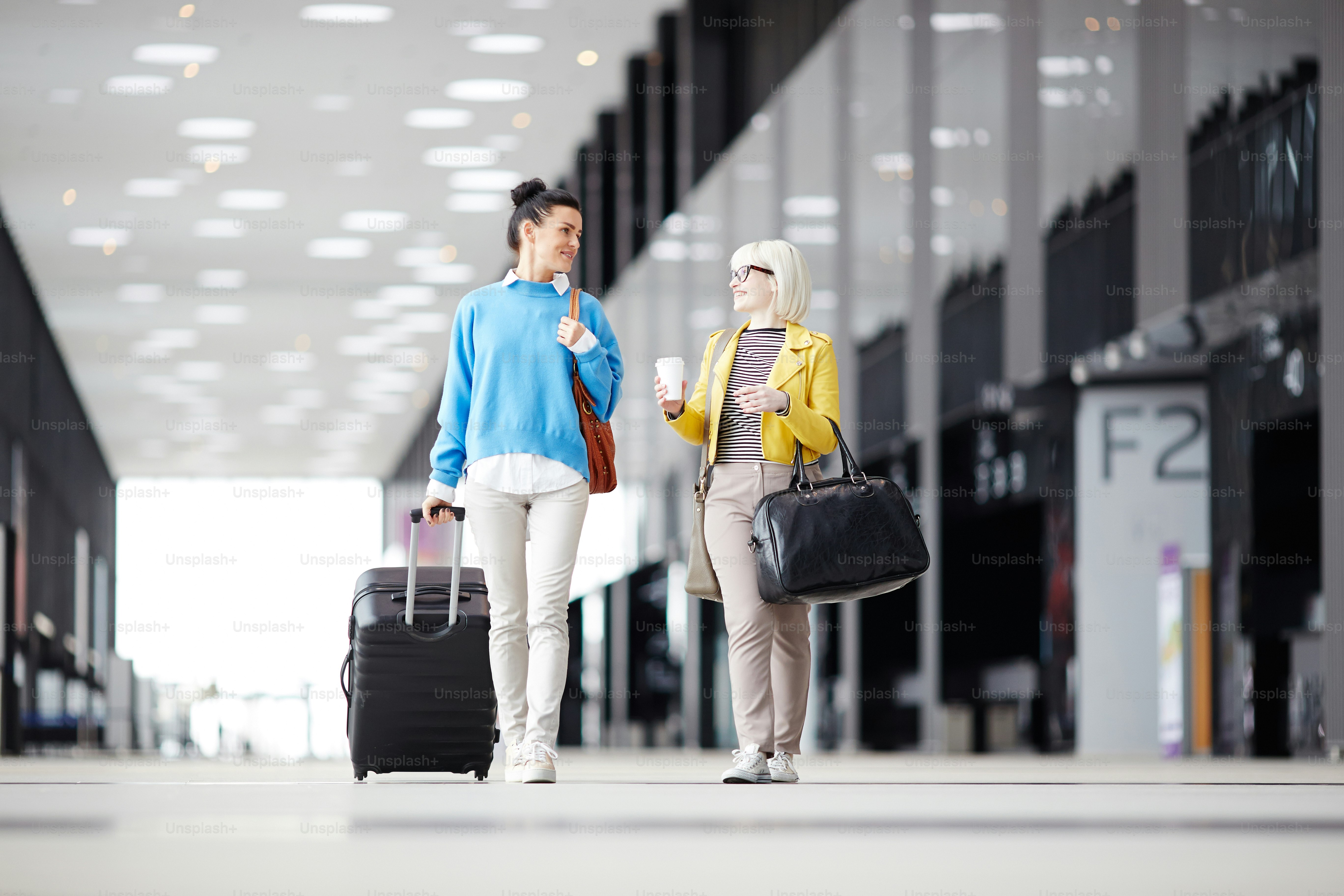 Two girls with baggage walking along airport building before or after ...