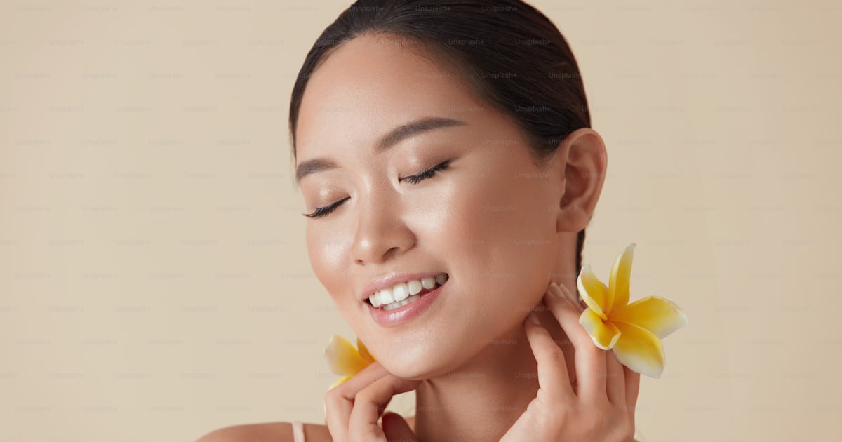 여자와 꽃 아름다움 초상화입니다 완벽한 빛나고 촉촉한 얼굴 피부를 가진 아름다운 민족 소녀 베이지색 배경에 열대 플루메리아를