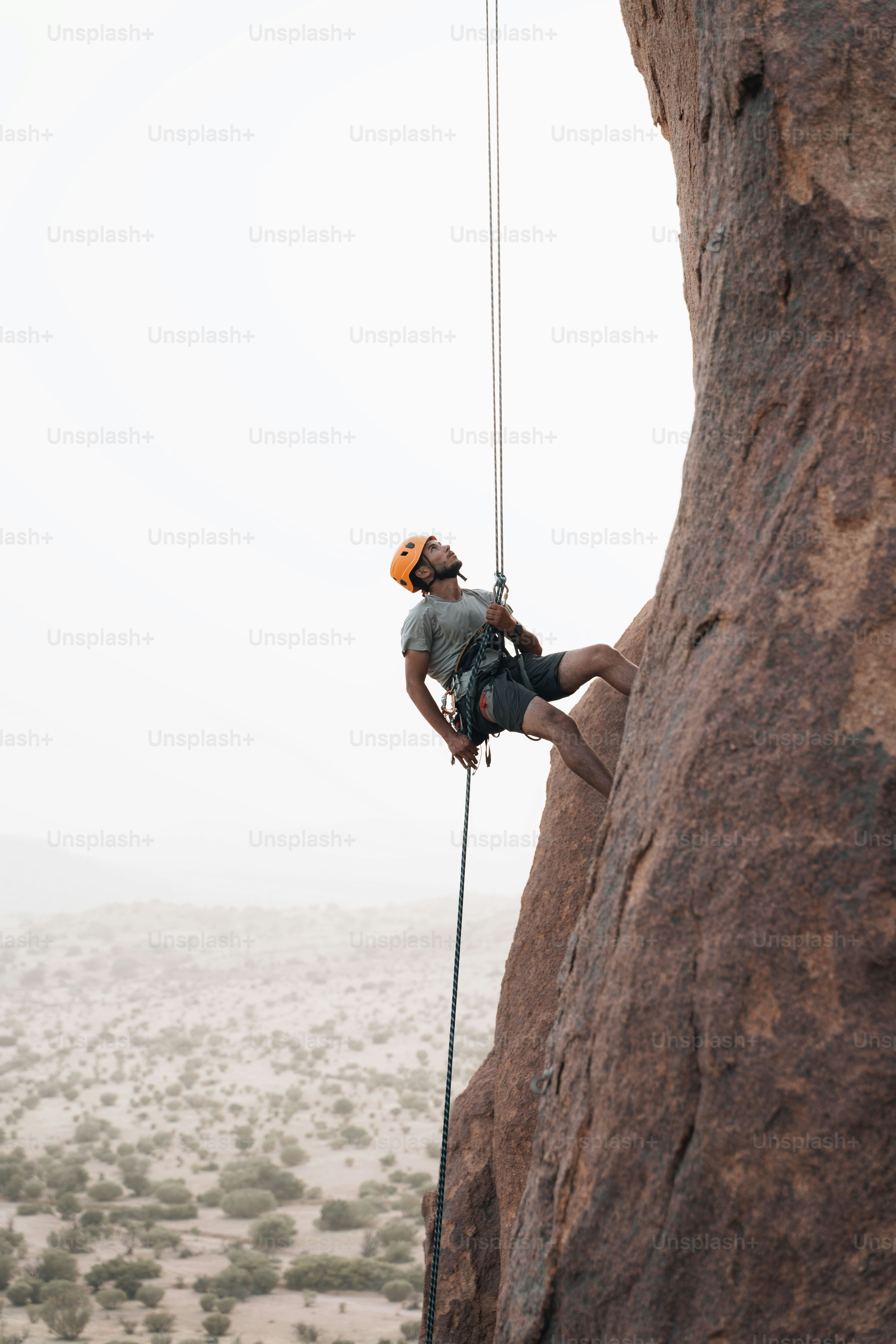 A man climbing up the side of a large rock photo – Rope Image on Unsplash