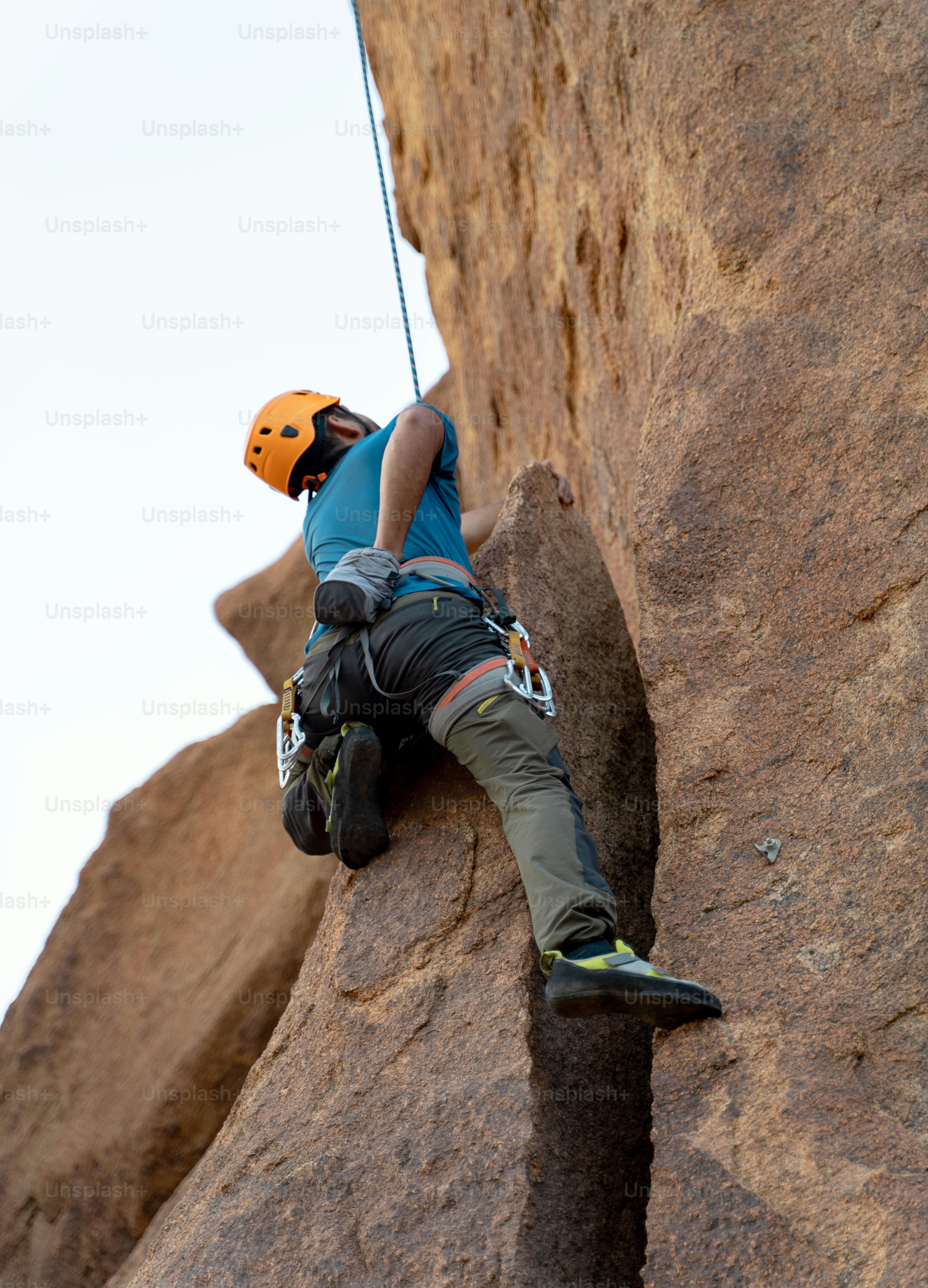 A man climbing up the side of a large rock photo – Rope Image on Unsplash