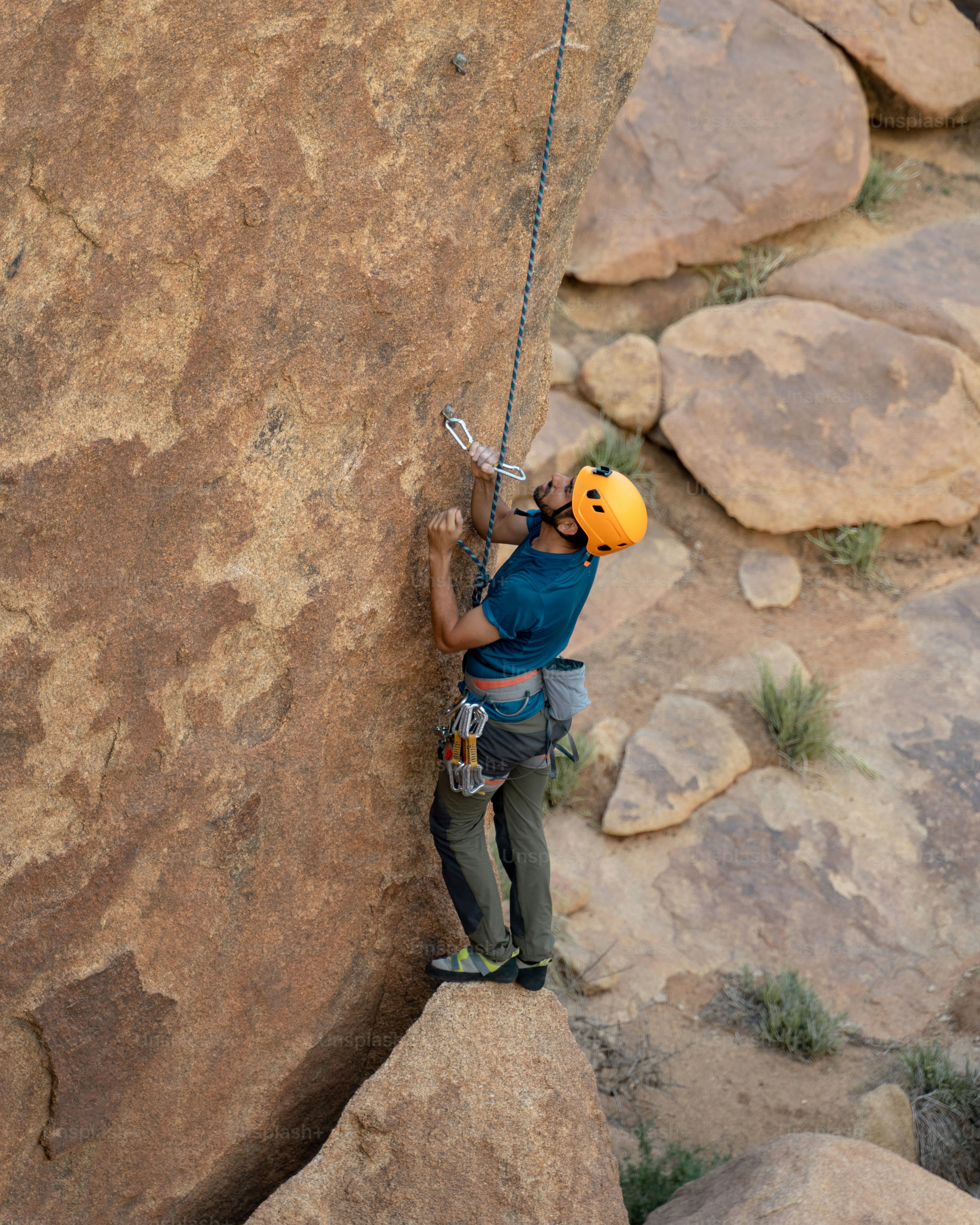 A man climbing up the side of a large rock photo – Climbing Image on ...