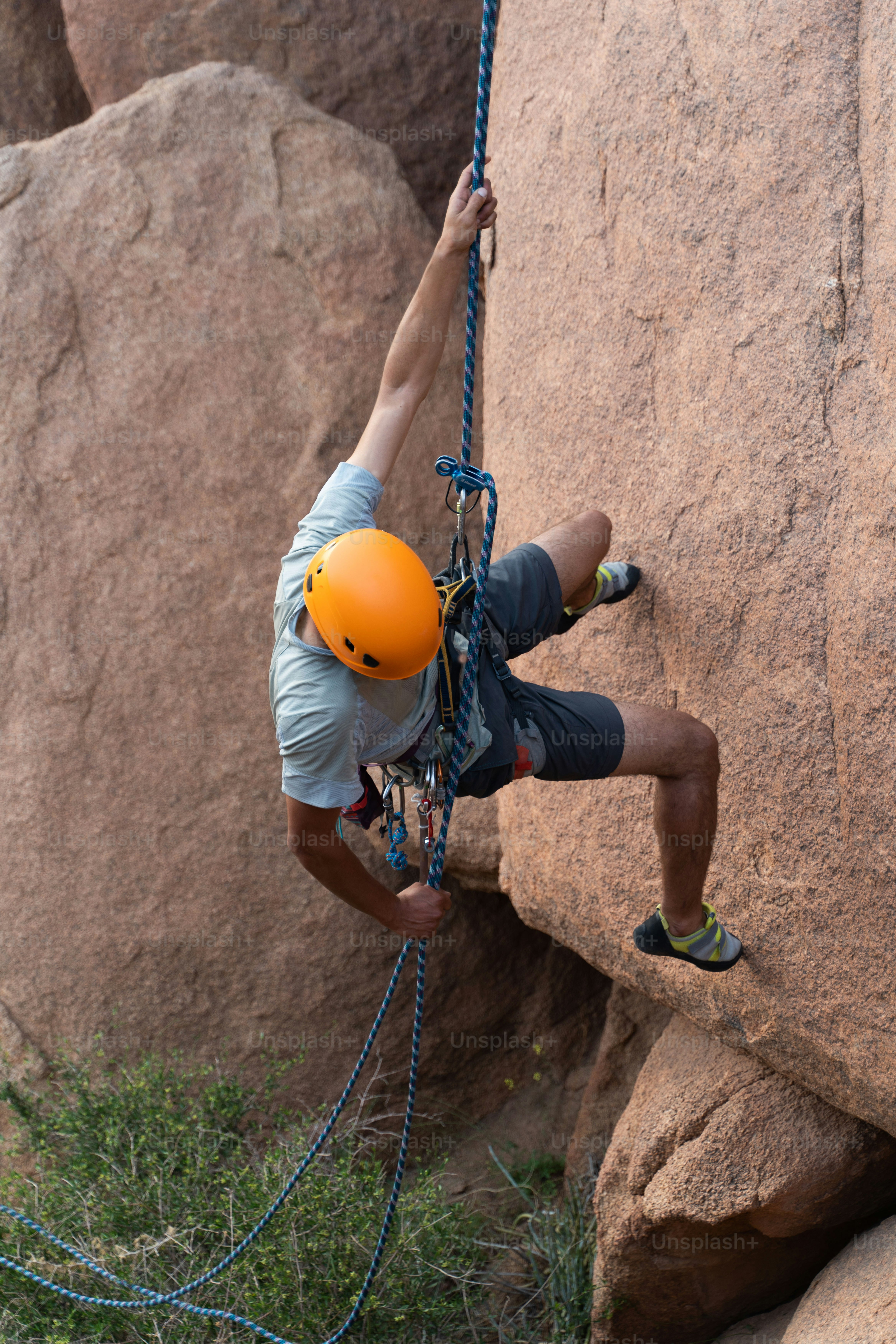 A man climbing up the side of a large rock photo – Climbing Image on ...